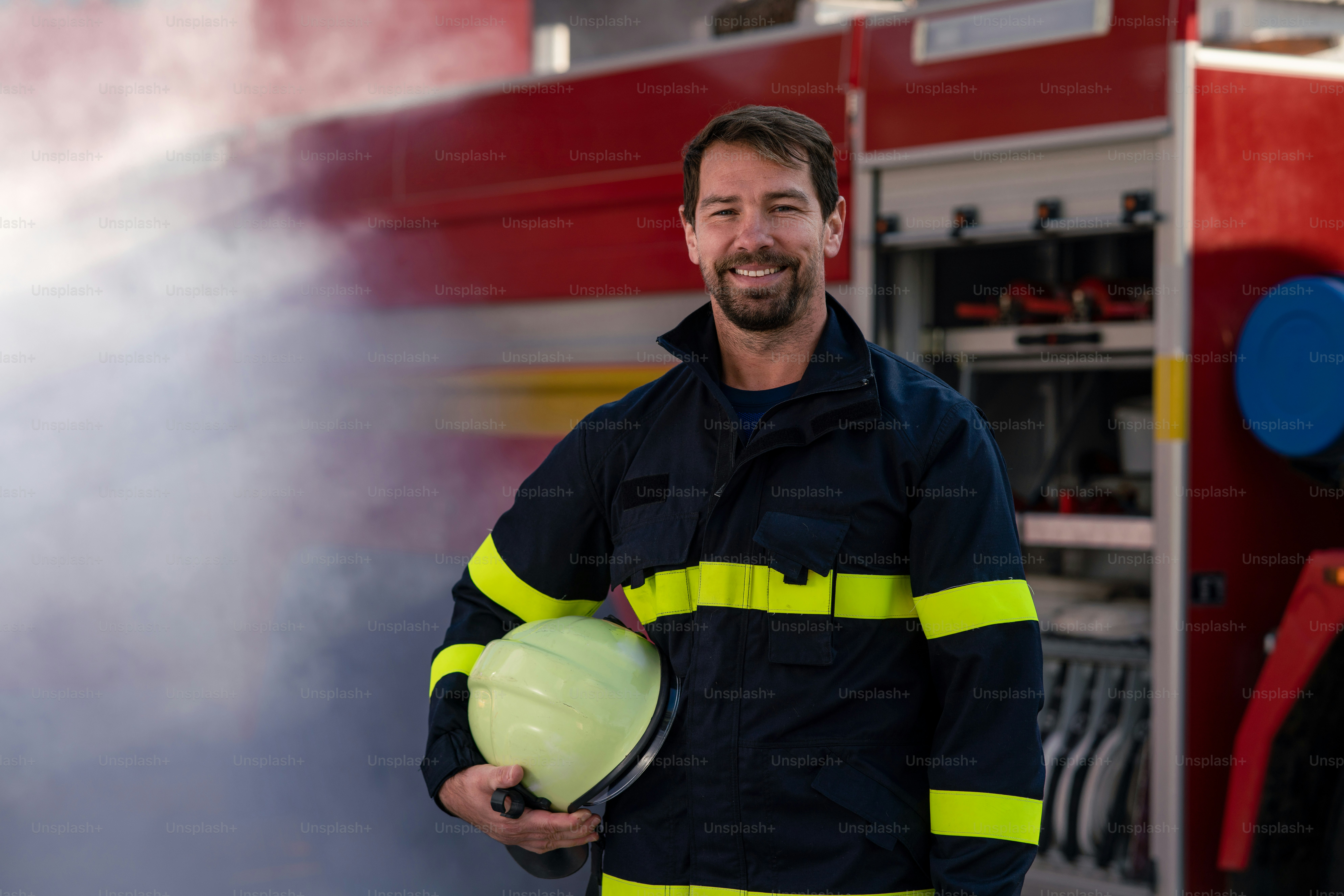 A happy mid-adult firefighter man looking at camera with fire truck and ...