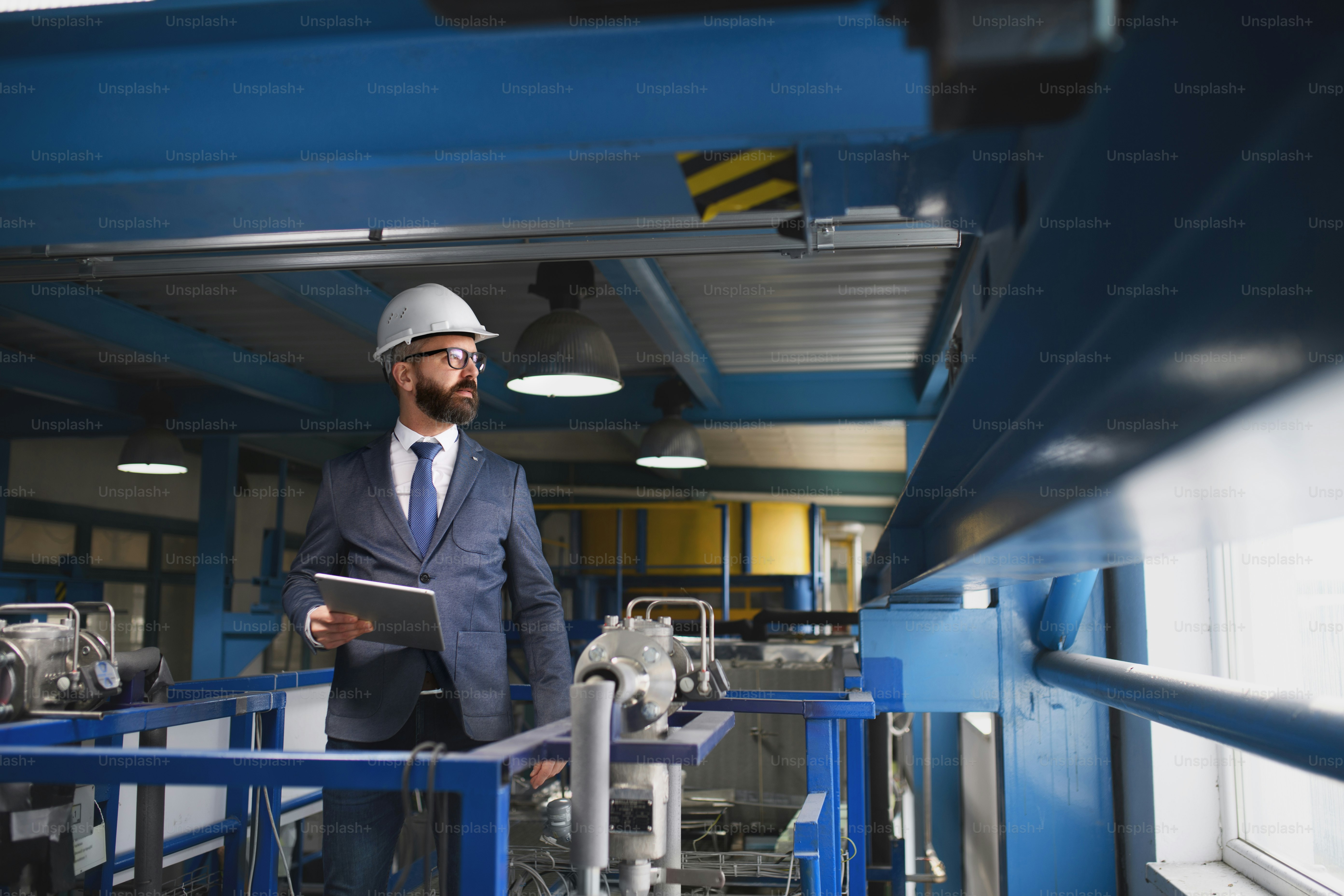 A chief Engineer in the hard hat walks through industrial factory while holding tablet. photo ...