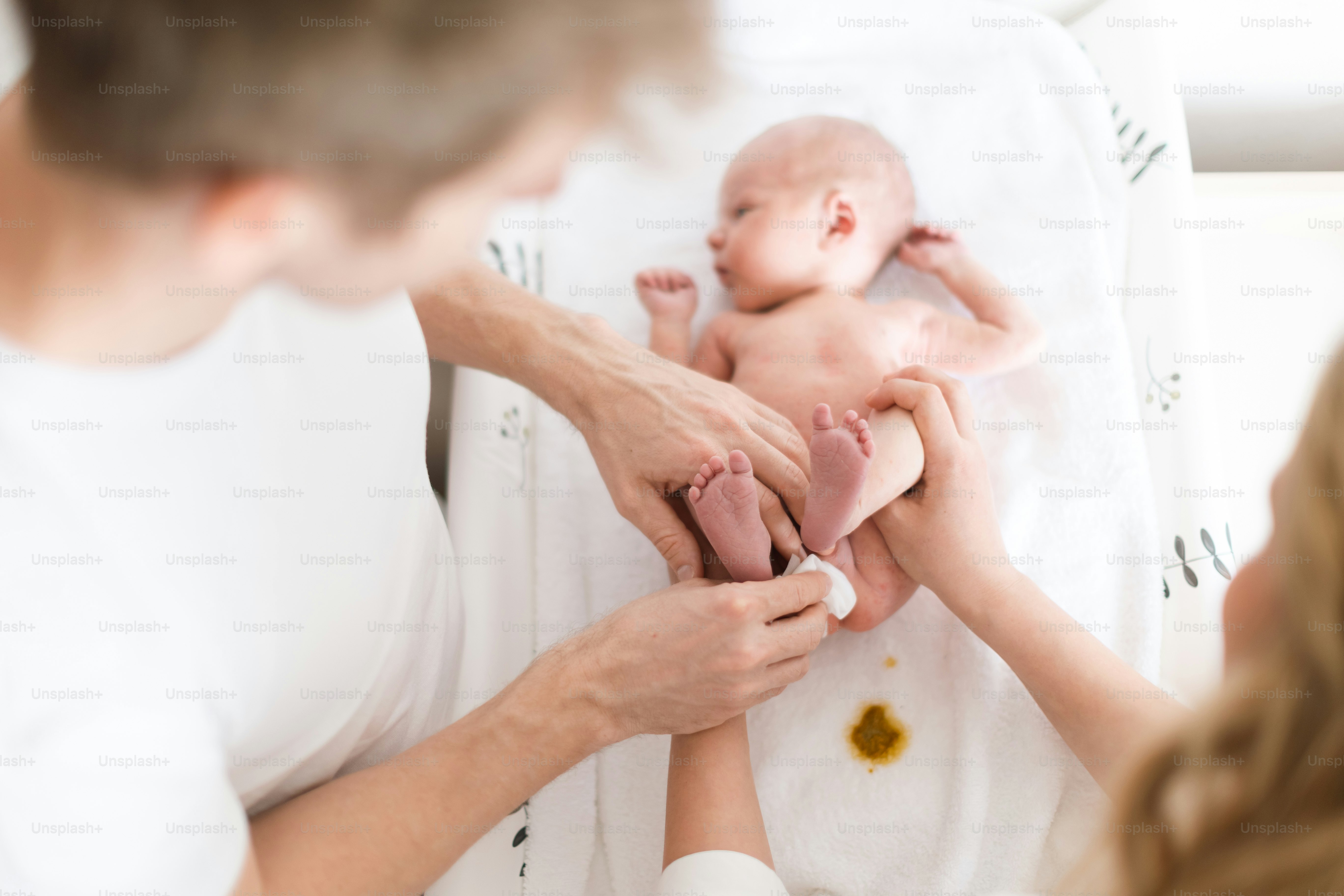 Parents together cahnging a nappy to newborn son who is lying on ...