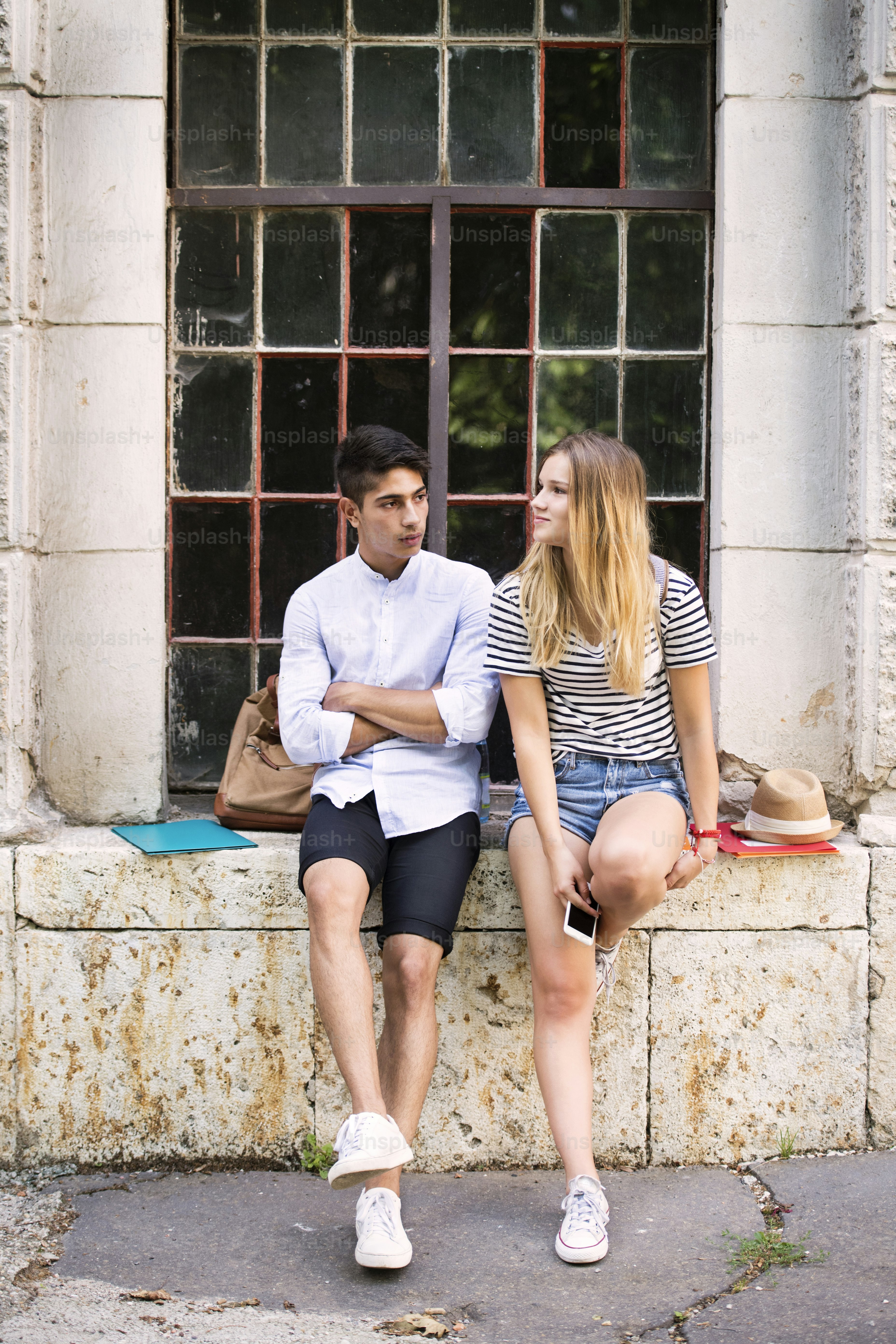 Group of attractive teenage students sitting on stone steps in front of ...