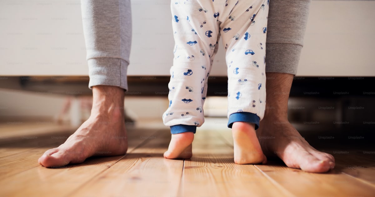 自宅の寝室の床に立っている見分けのつかない父親とよちよち歩きの男の子の足。育児休暇。スペースをコピーします。の写真 Unsplashの子供の画像