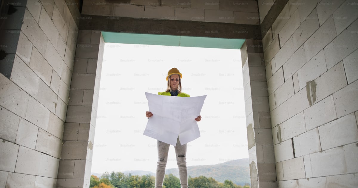 建築現場の女性作業員。青写真を保持している美しい若い女性。家の建設。の写真 衣類 Unsplashの写真