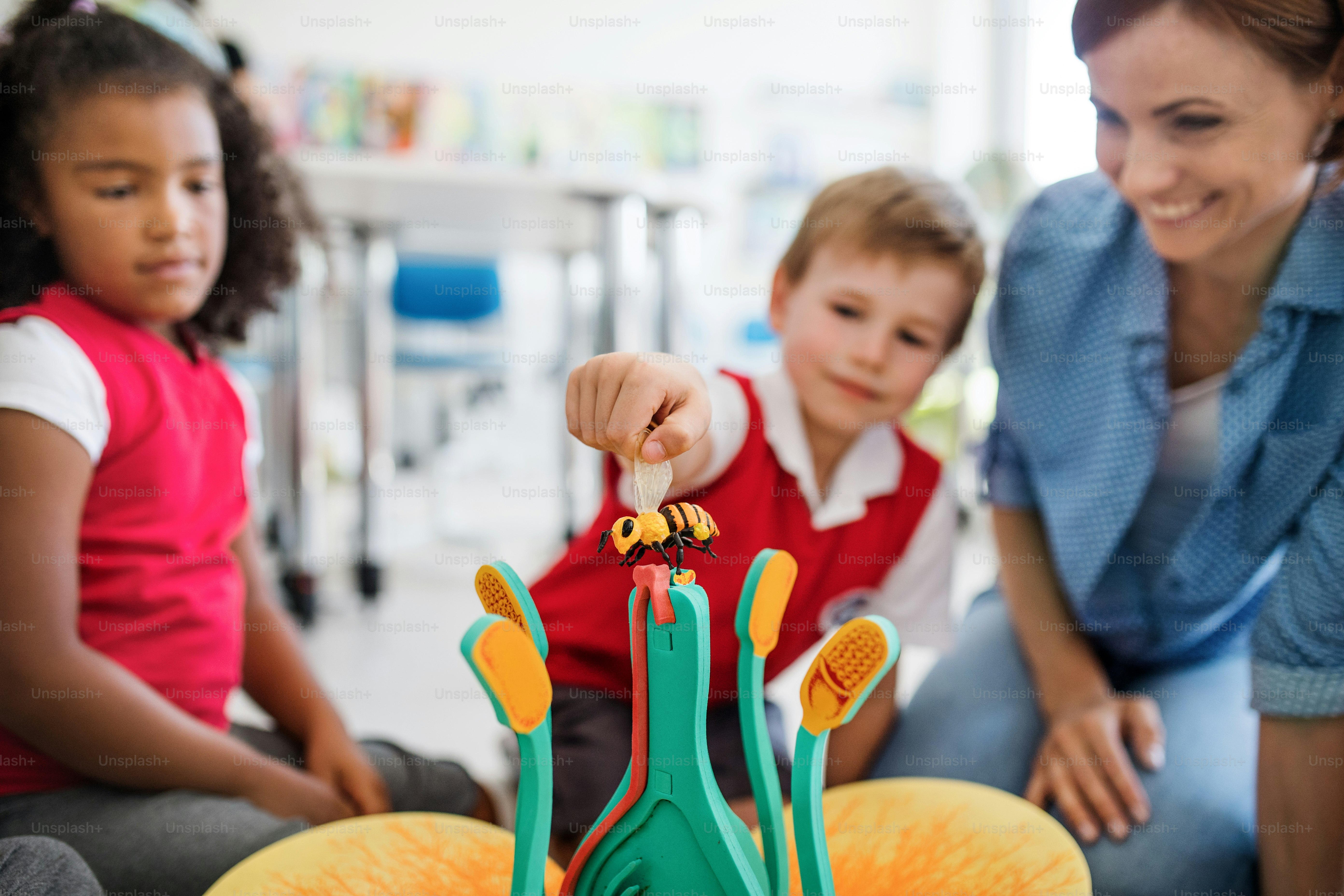 A group of small school kids with teacher sitting on the floor in class ...