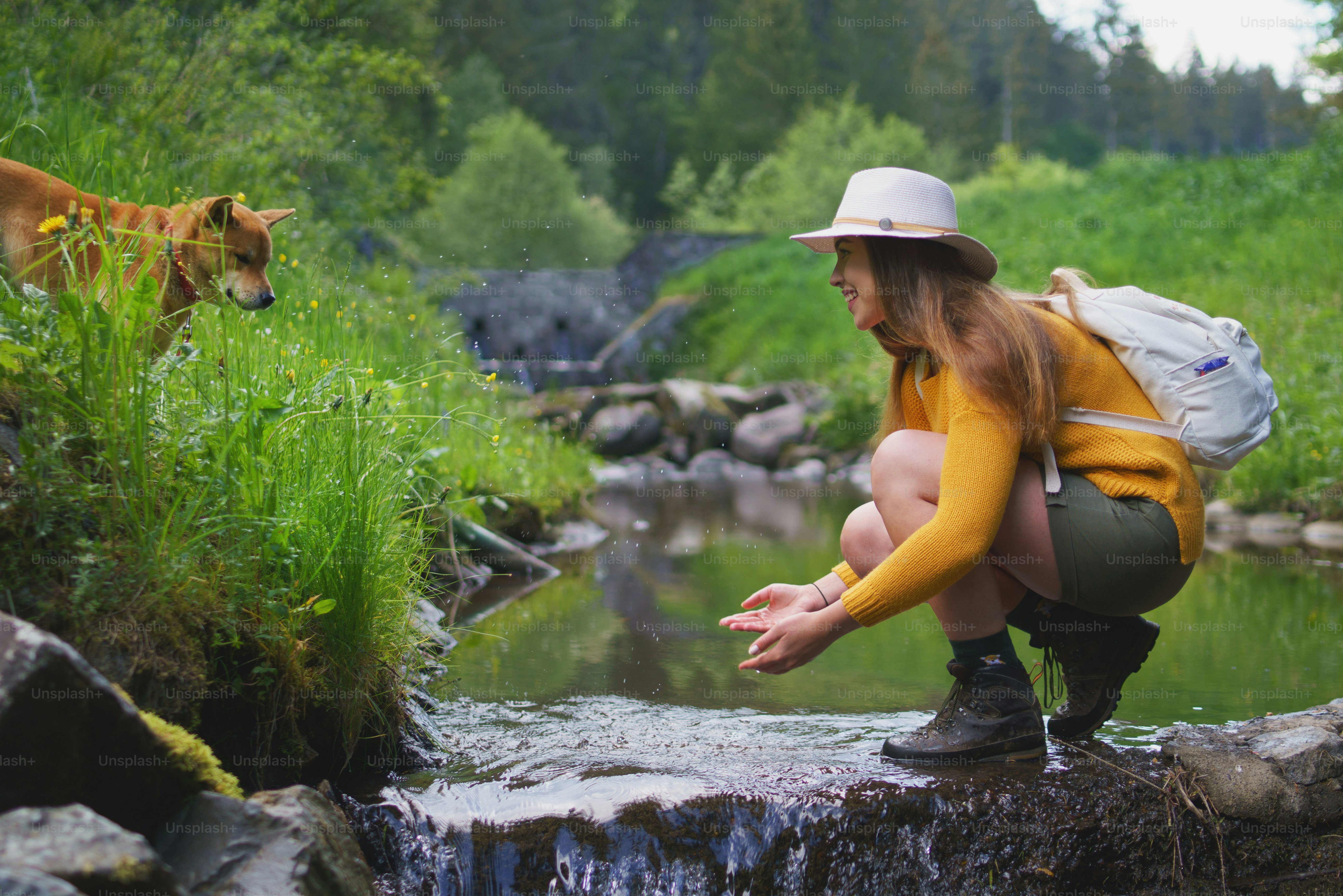 Happy young woman standing by stream on a walk outdoors in summer ...