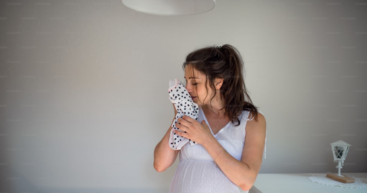 女の子のボディー スーツを保持している自宅で室内で妊娠中の女性の正面図の肖像画。の写真 スロバキア Unsplashの写真