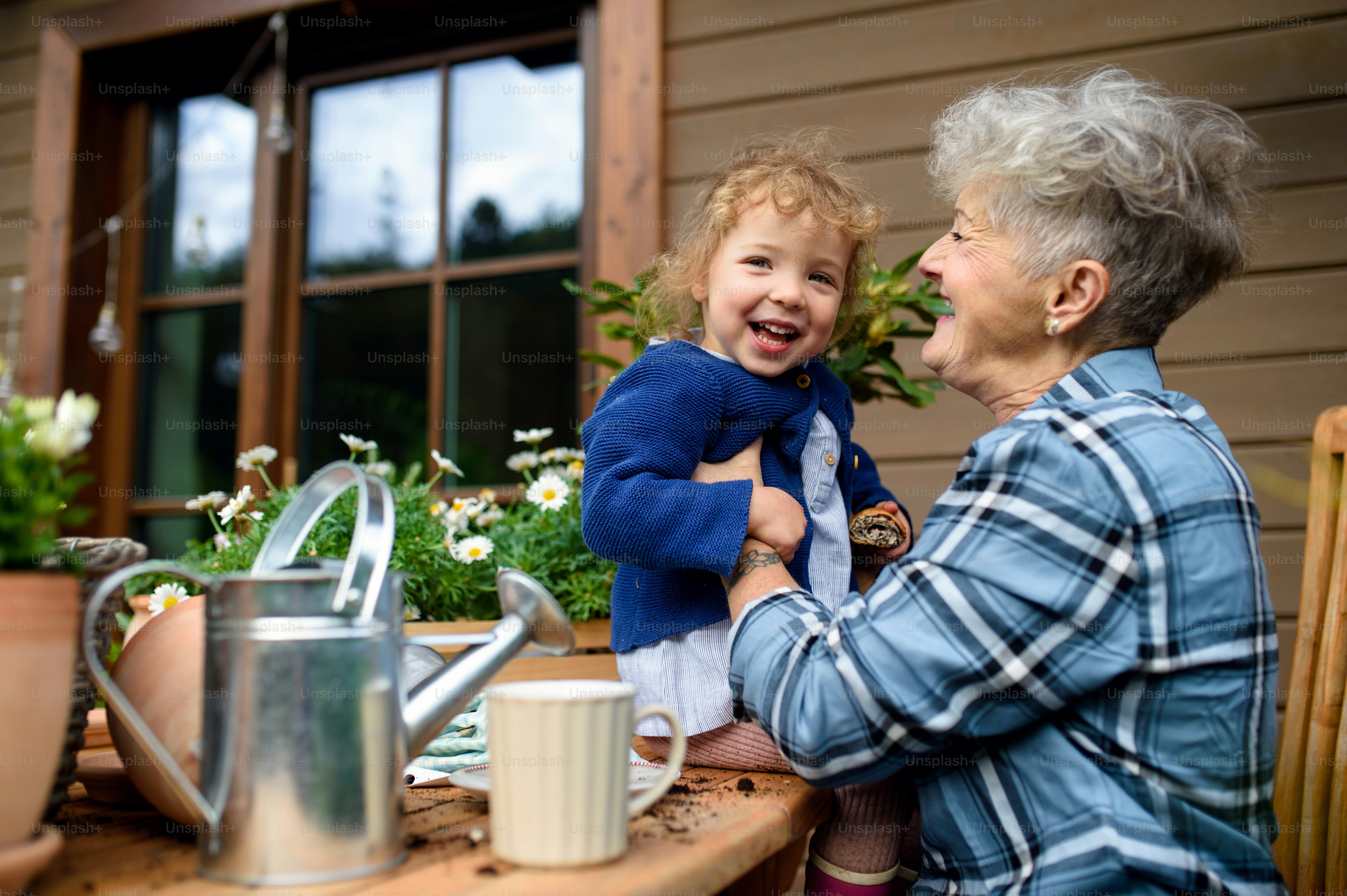 Happy senior grandmother with small granddaughter gardening on terrace ...