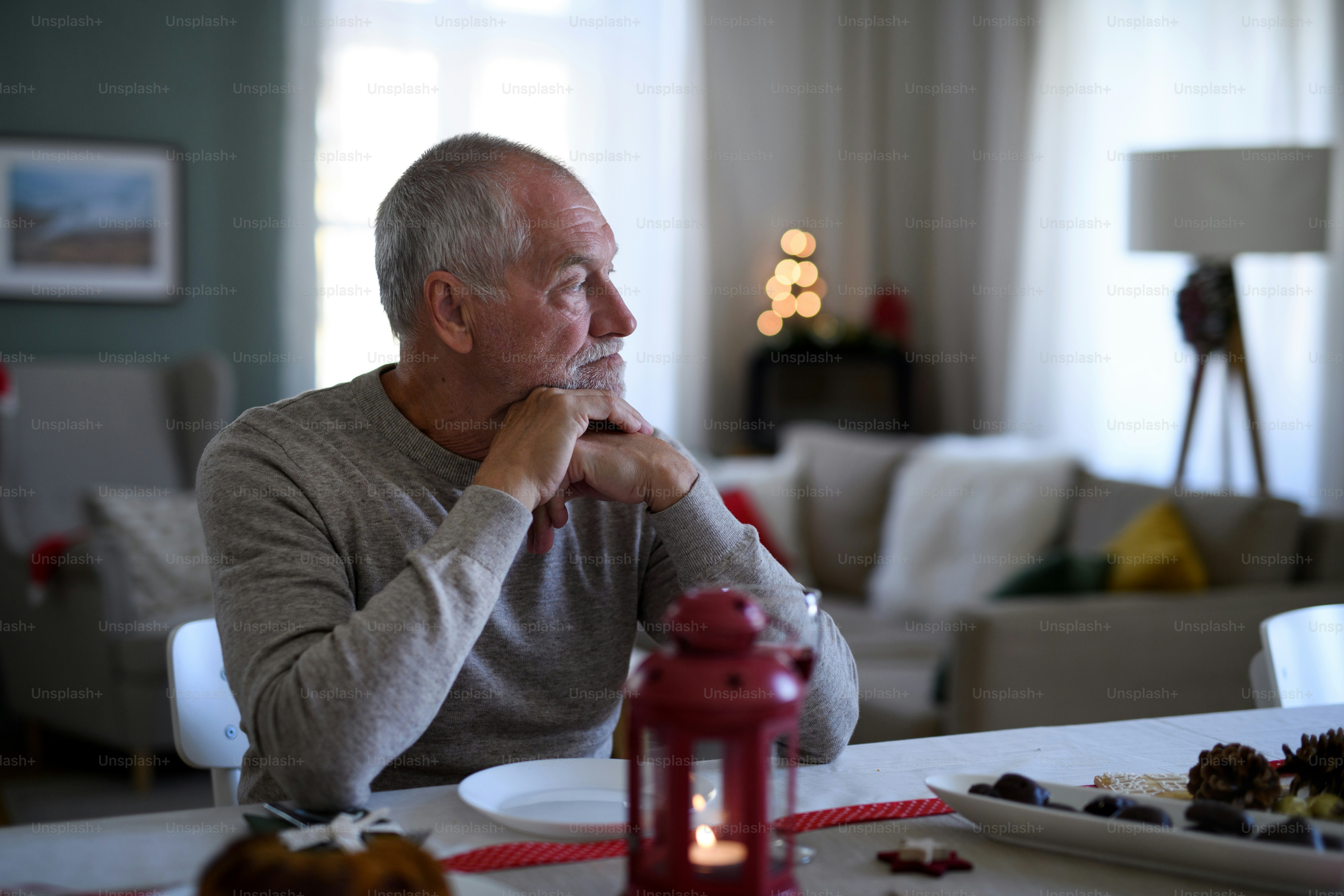 Portrait of lonely senior man sitting at the table indoors at Christmas ...