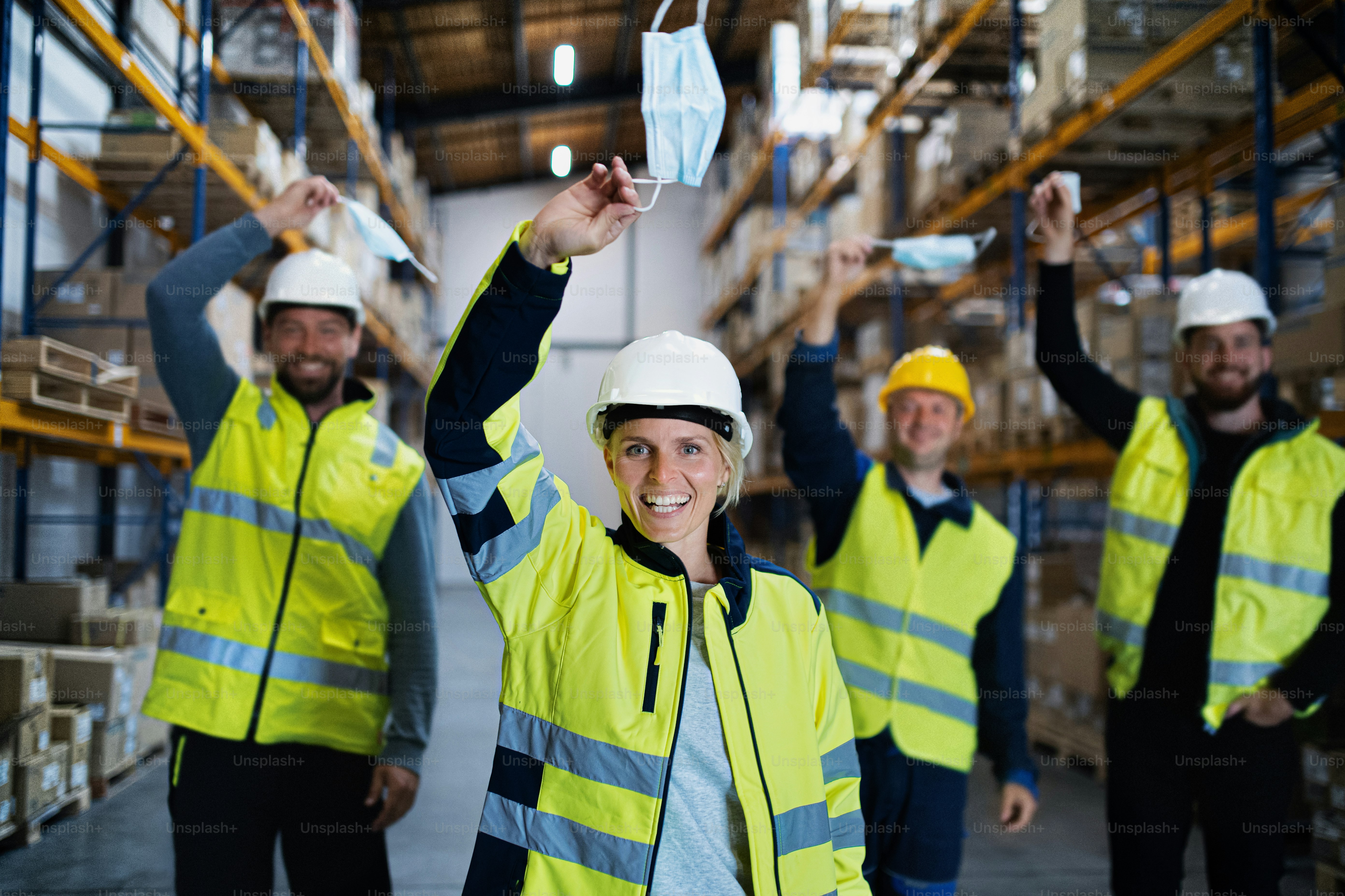 Group of workers jumping and taking face masks off indoors in warehouse ...