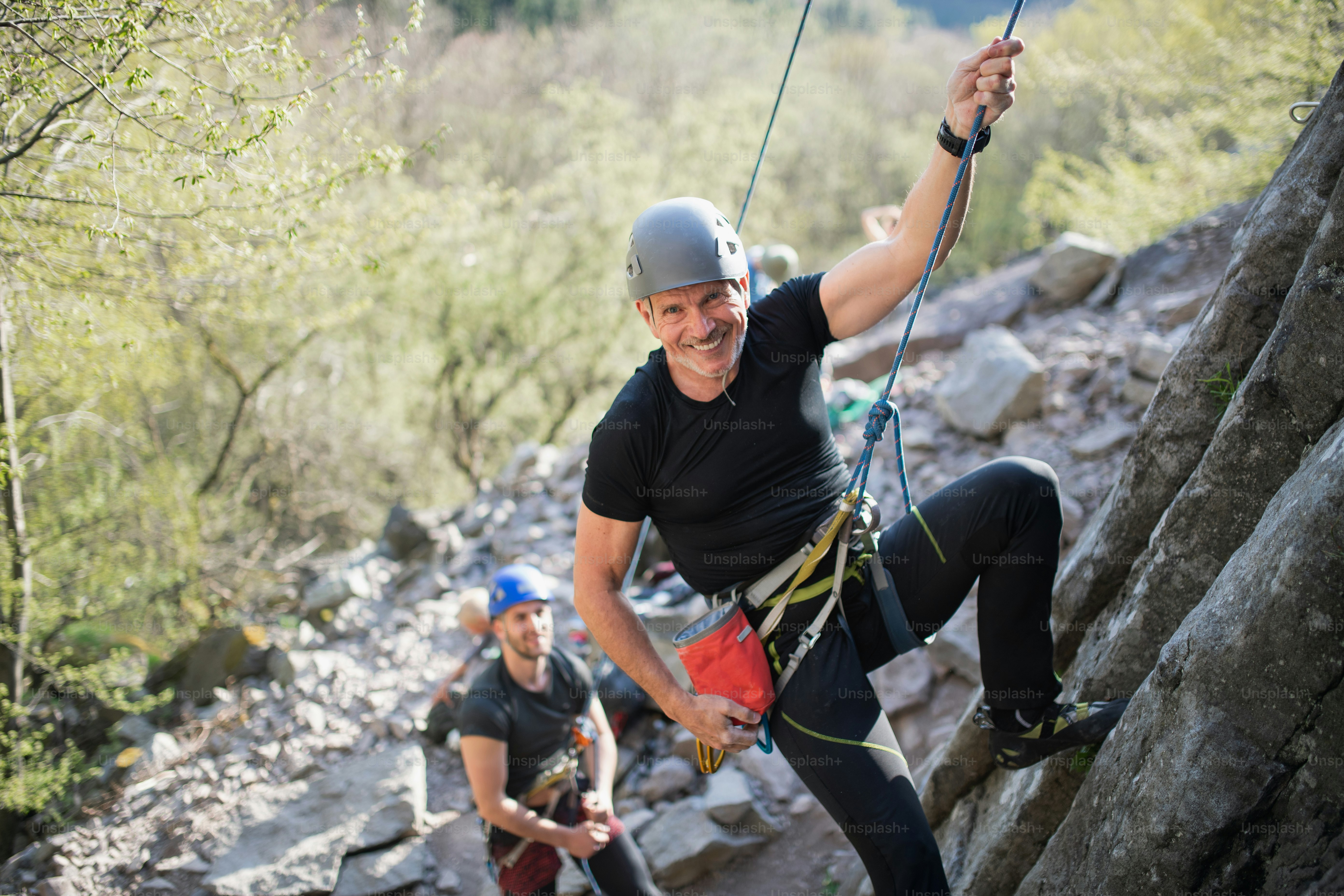 Portrait of senior man with instructor climbing rocks outdoors in ...