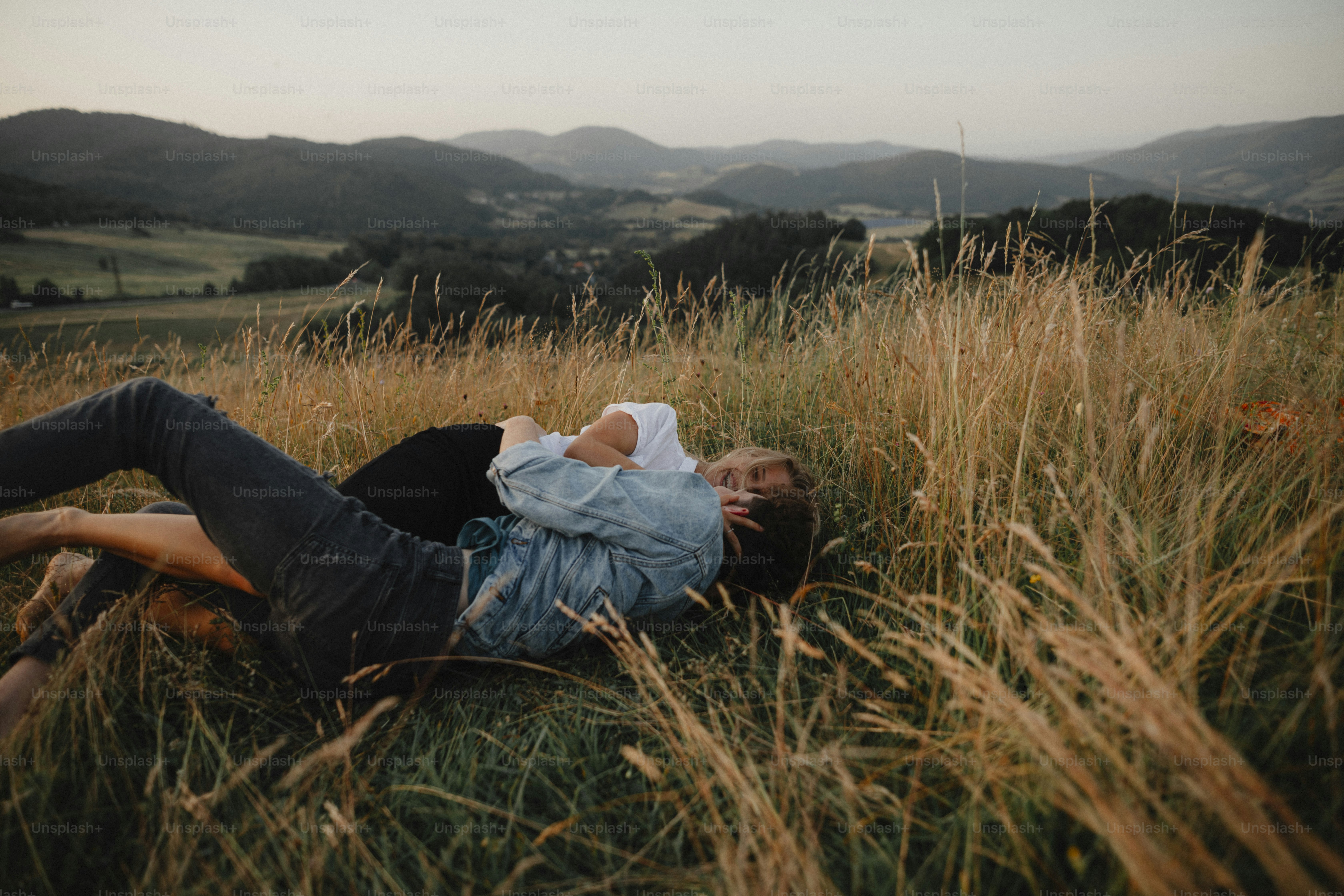A young couple on a walk in nature in countryside, lying in grass ...
