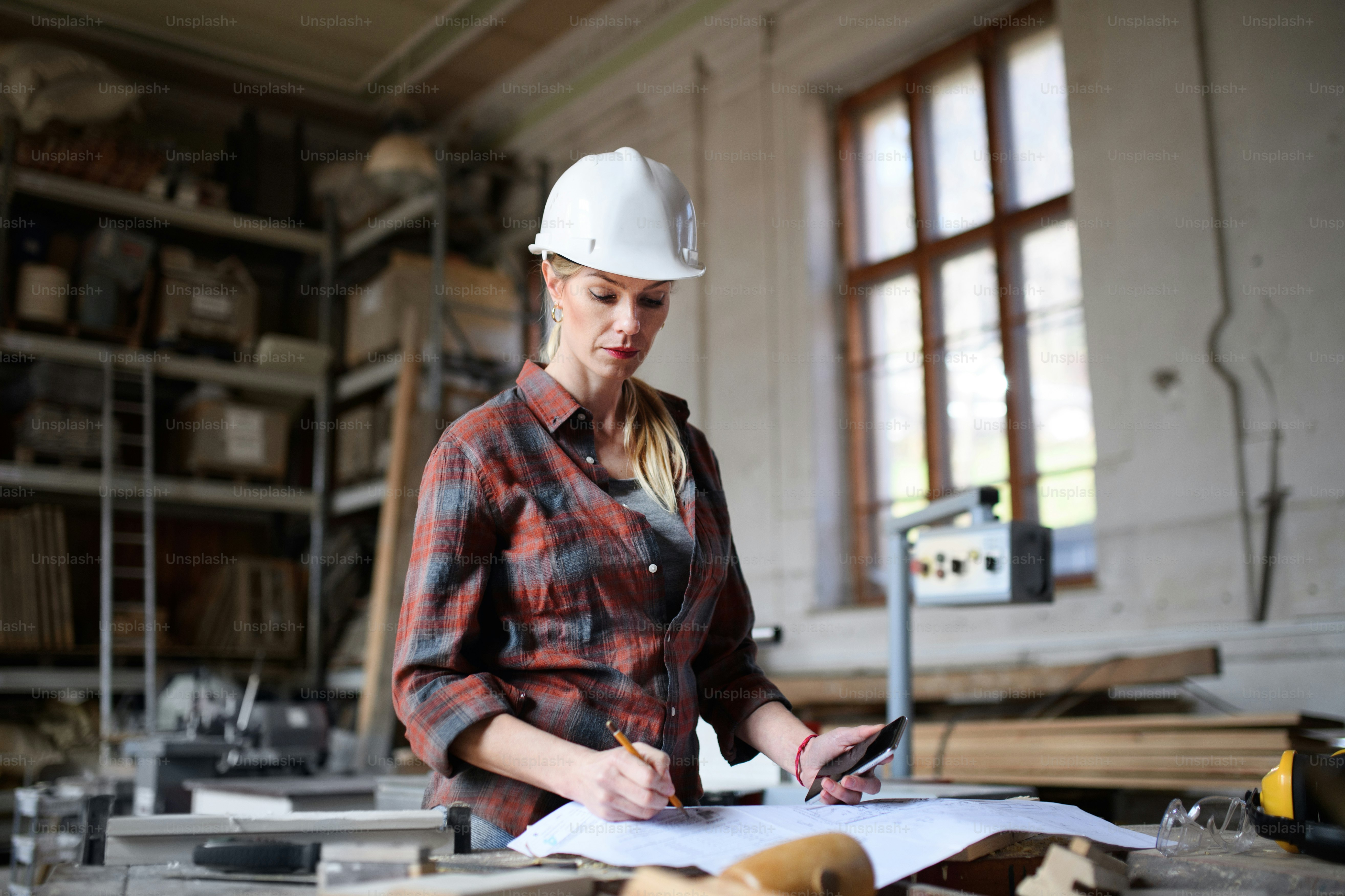 A portrait of female engineer looking at blueprints indoors in ...
