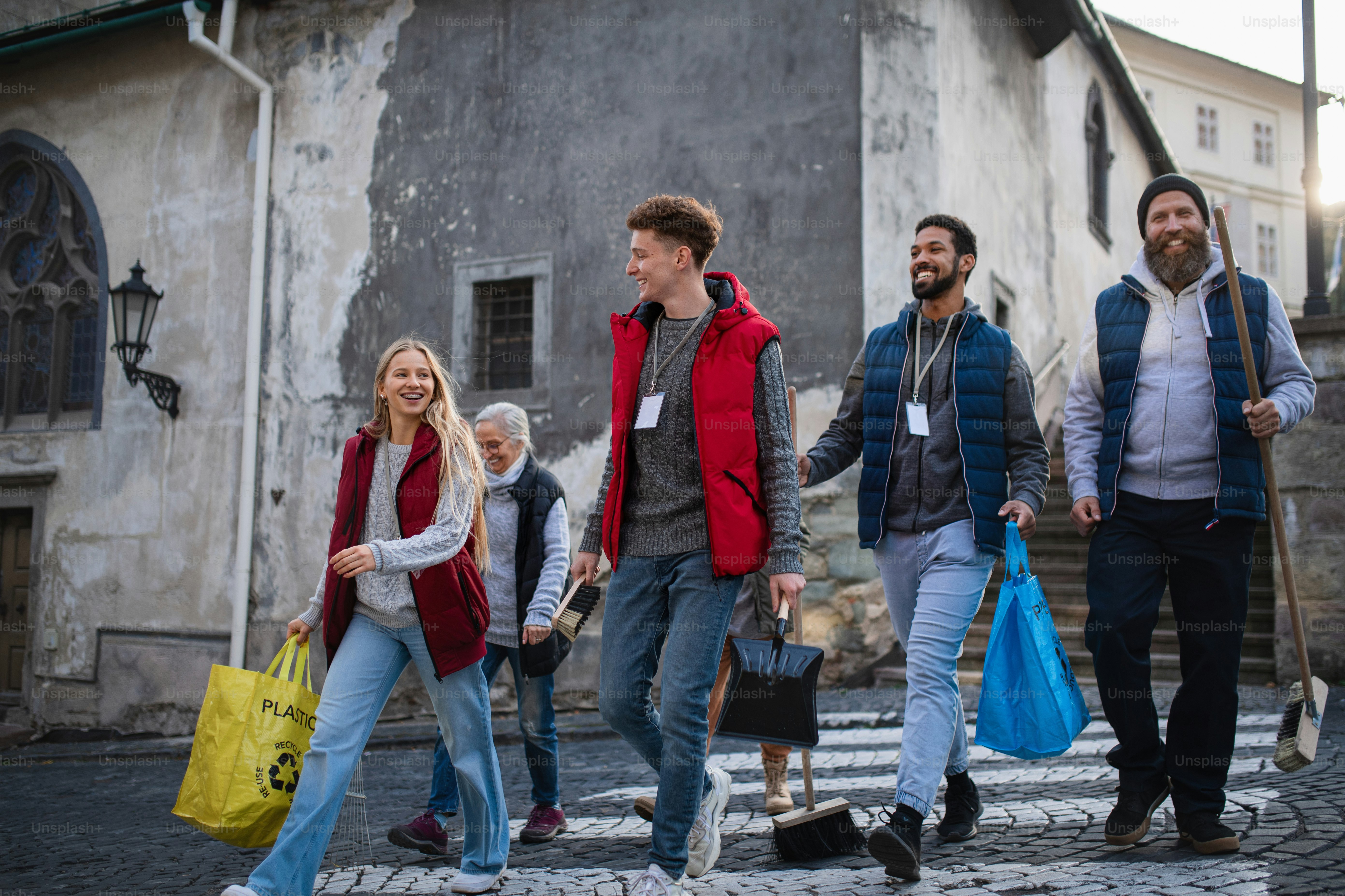 A diverse group of happy volunteers walking with tools to do street ...