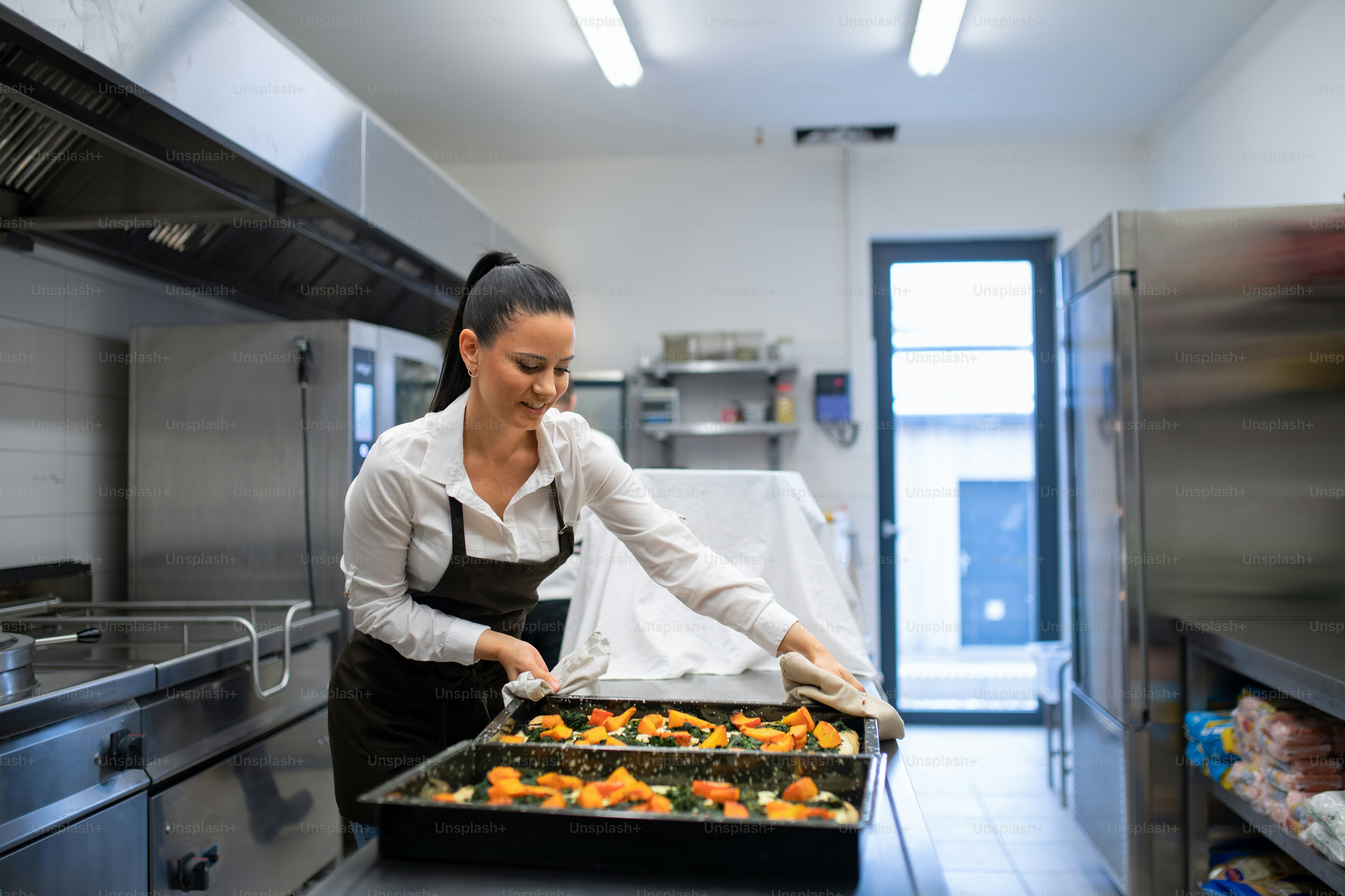 A professional chef working on her dishes indoors in restaurant kitchen ...