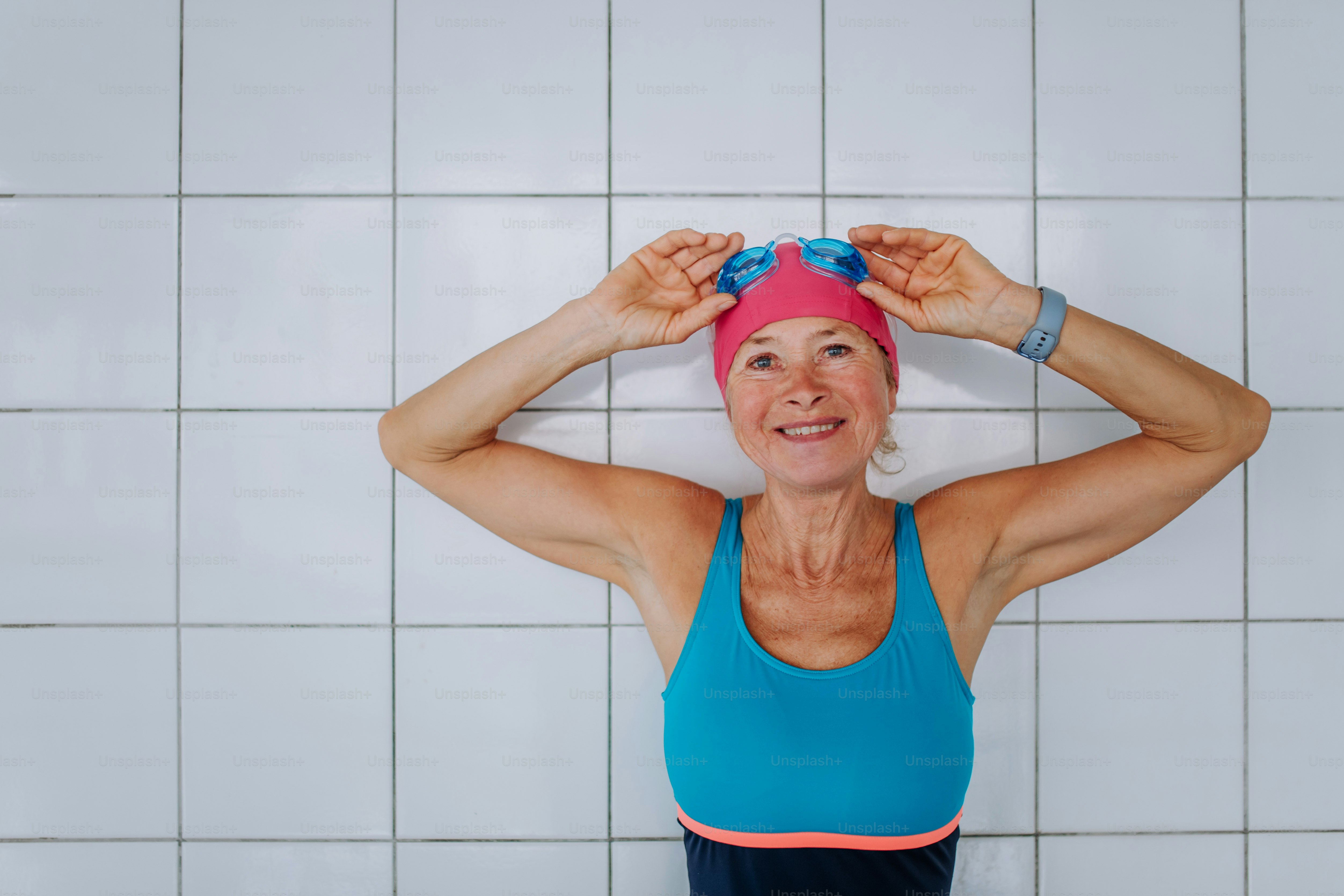 An active senior swimmer woman standing against white tiles wall in ...