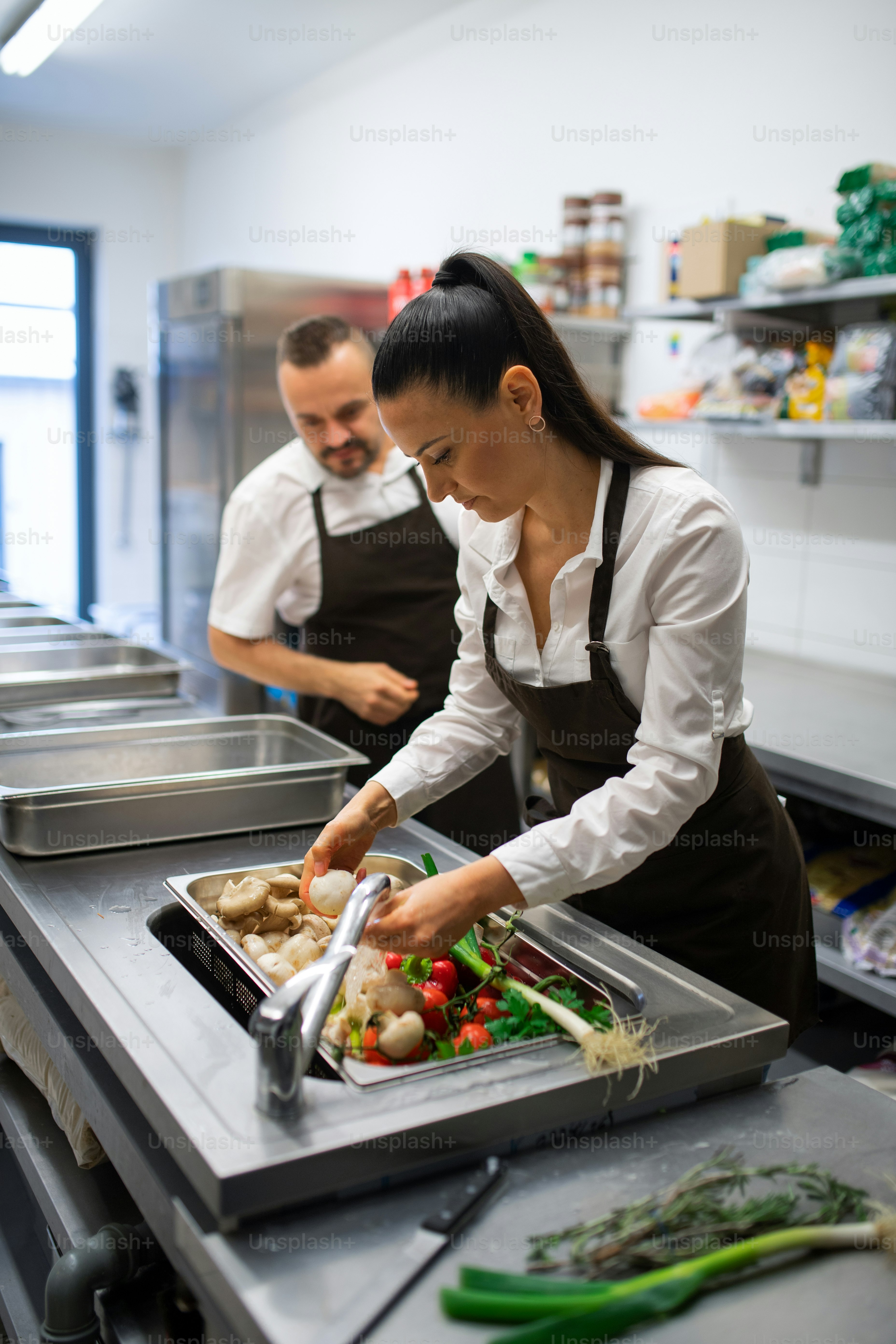 A close-up of cook washing vegetables in sink in commercial kitchen ...
