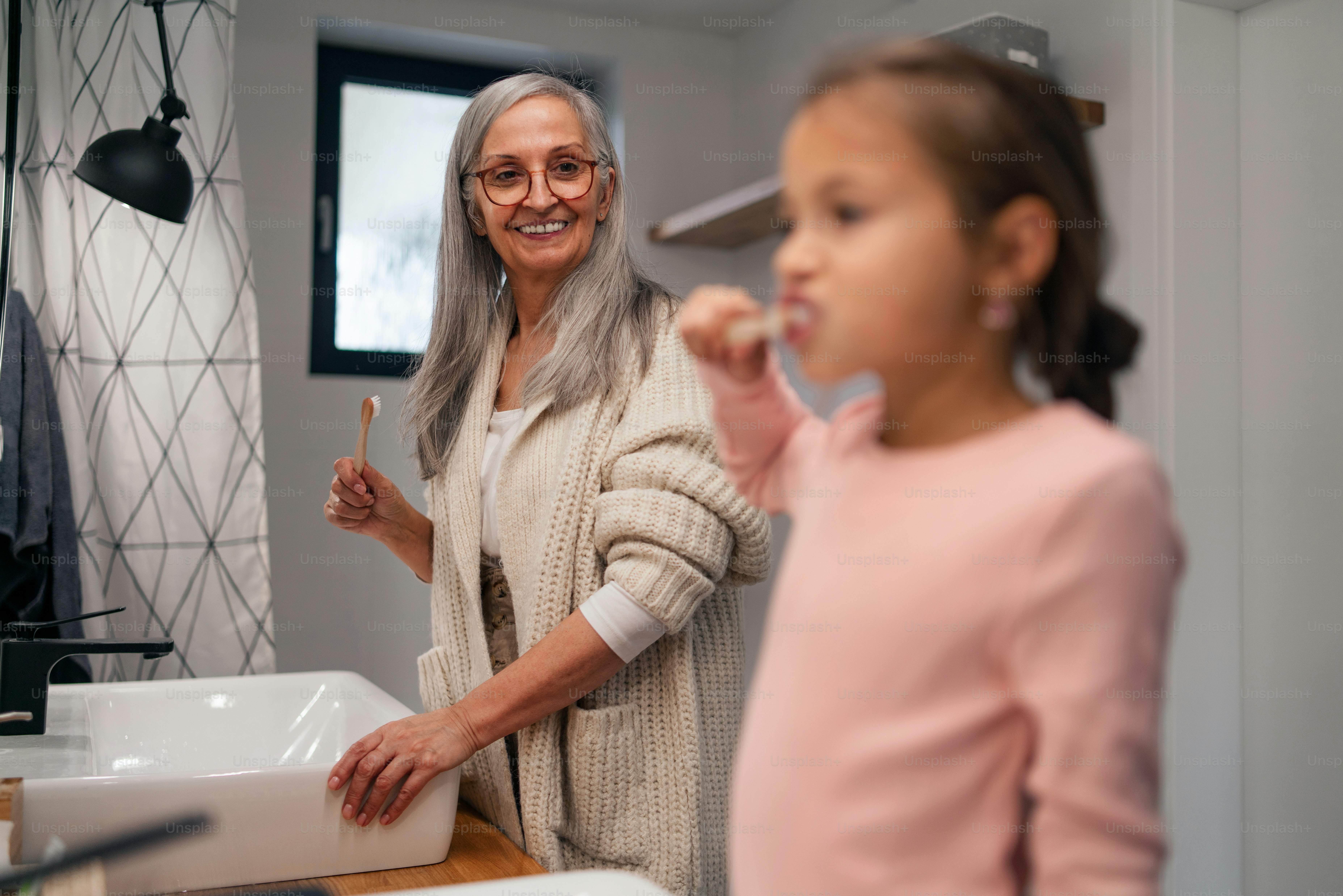 A senior grandmother making a ponytail to her granddaughter indoors in ...