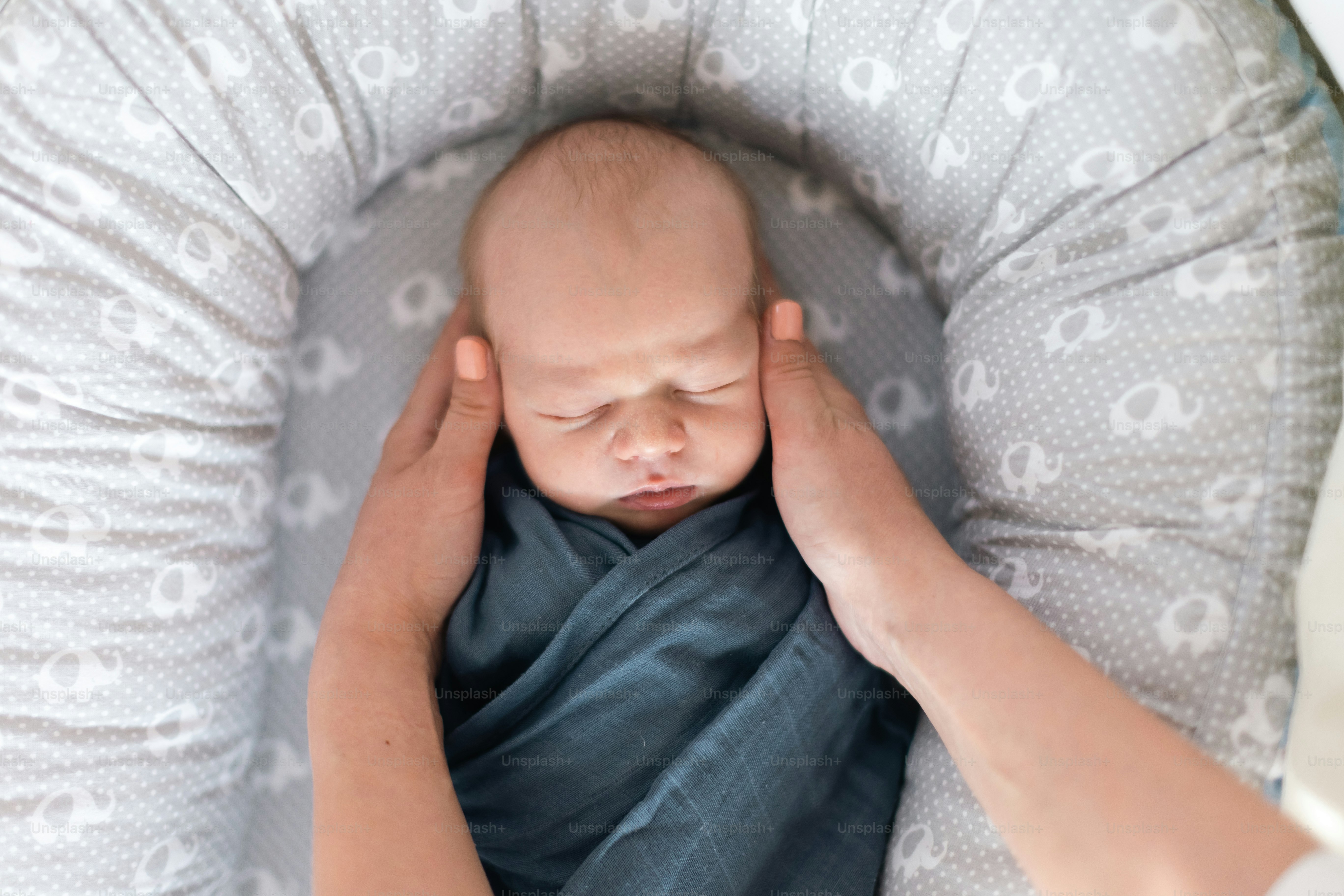 A newborn baby boy sleeping and swaddled in blue cloth lying in grey ...
