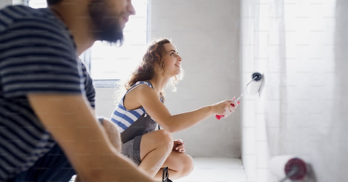 新居でペイントローラーを使って壁をペイントして楽しんでいる美しい若いカップル。家の模様替えとリノベーションのコンセプト。の写真 改築