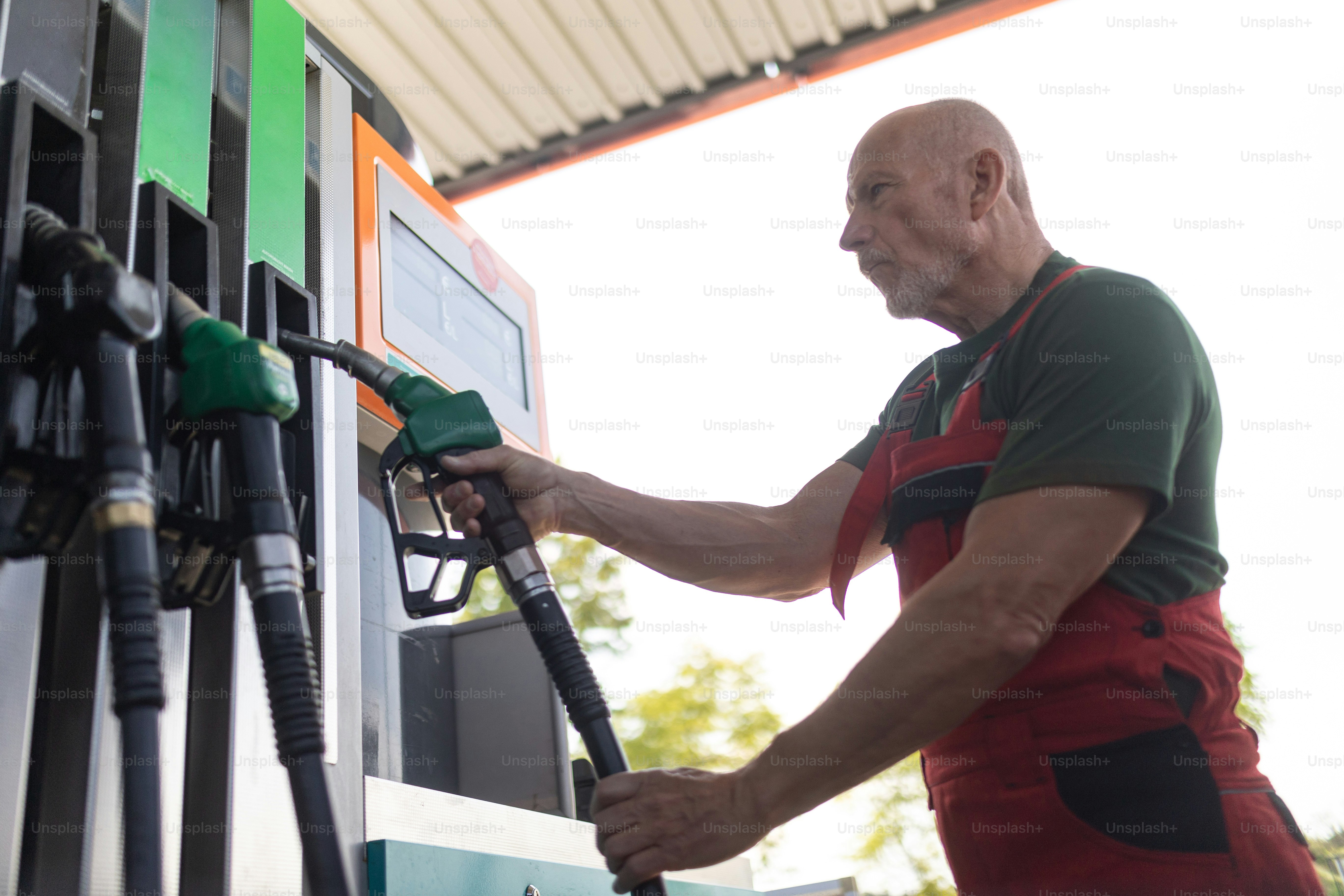 A senior worker standing on gas station and fueling car. photo – Fuel ...