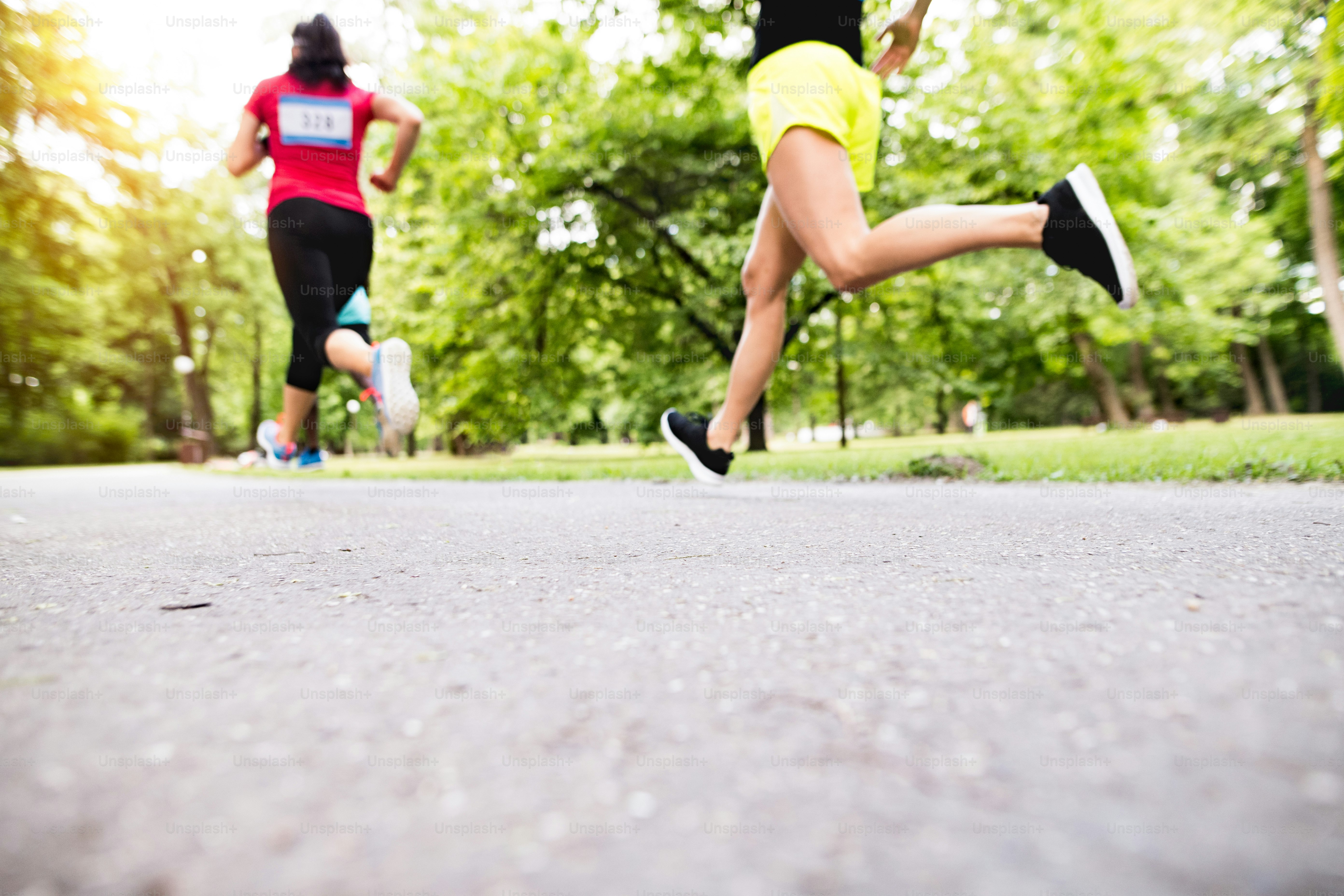 Close up of legs of young athletes running in green sunny summer park ...