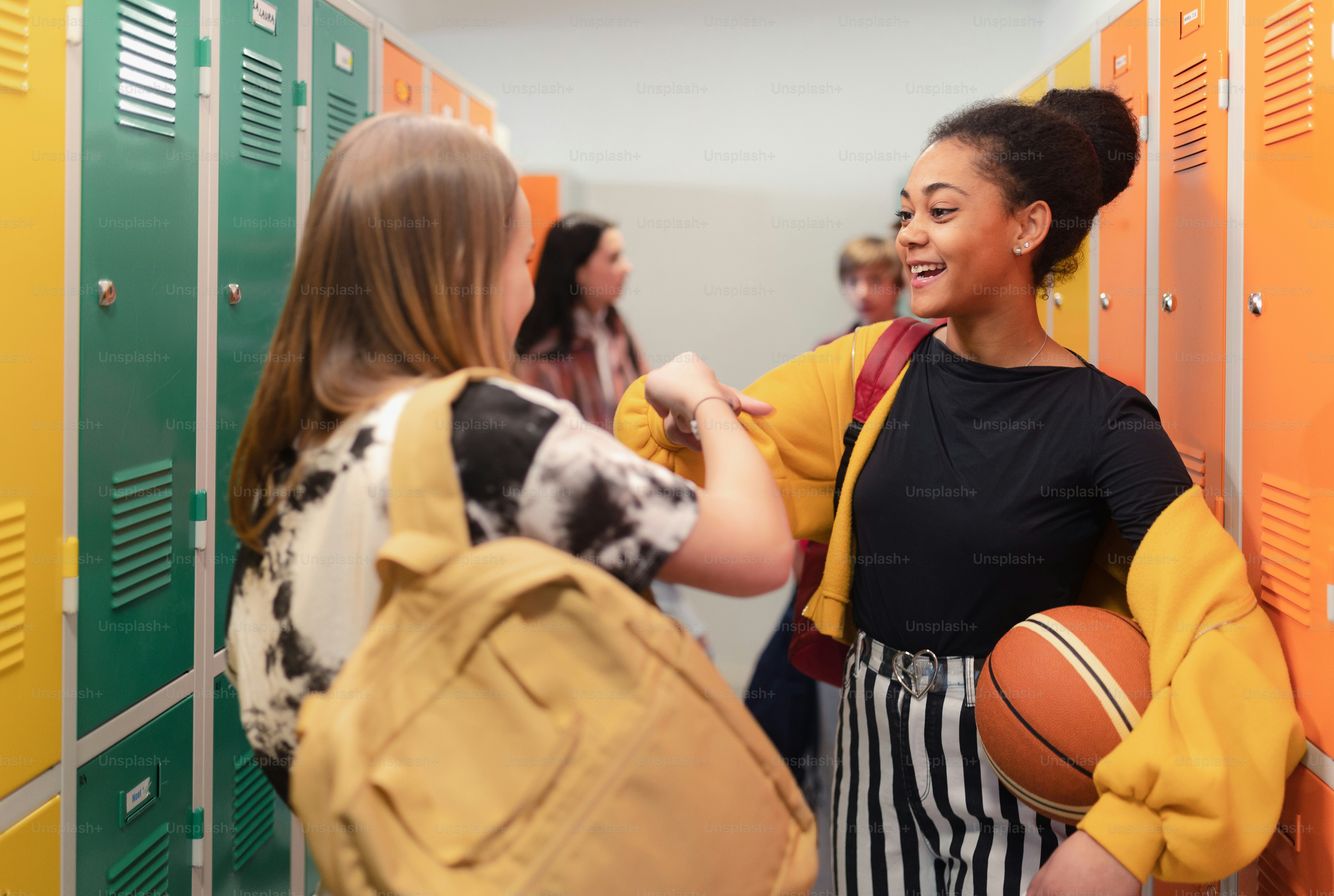 Young high school students meeting and greeting near a locker in campus ...