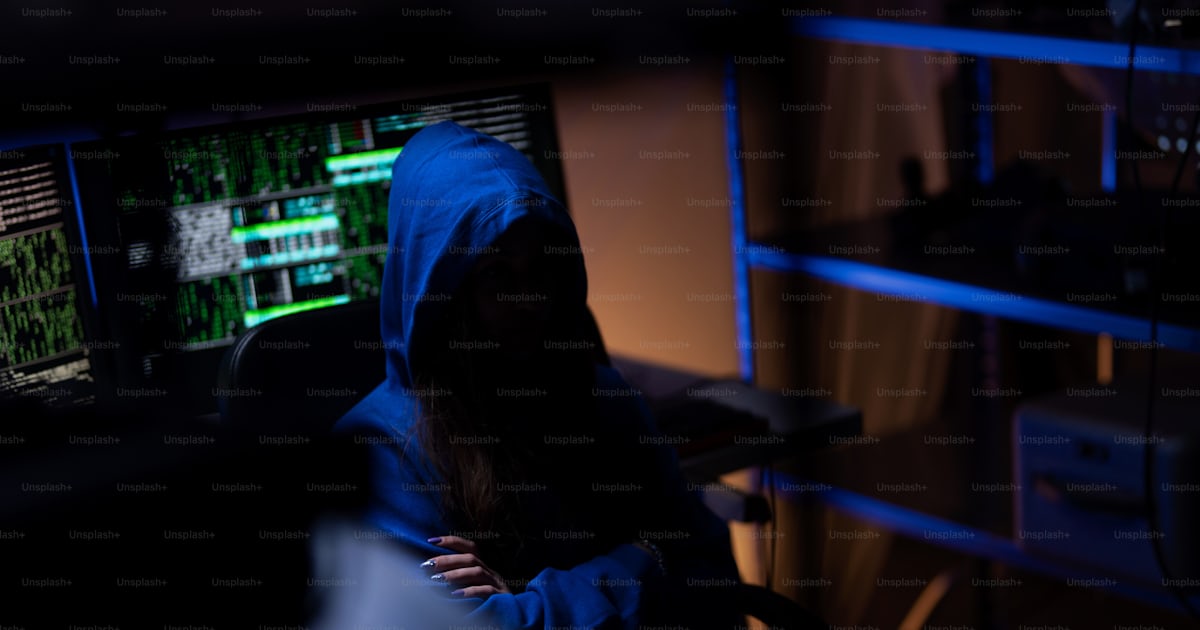 フードをかぶった匿名のハッカーが、夜の暗い部屋でコンピューターを操作し、サイバー戦争のコンセプトを描いている。の写真 スロバキア