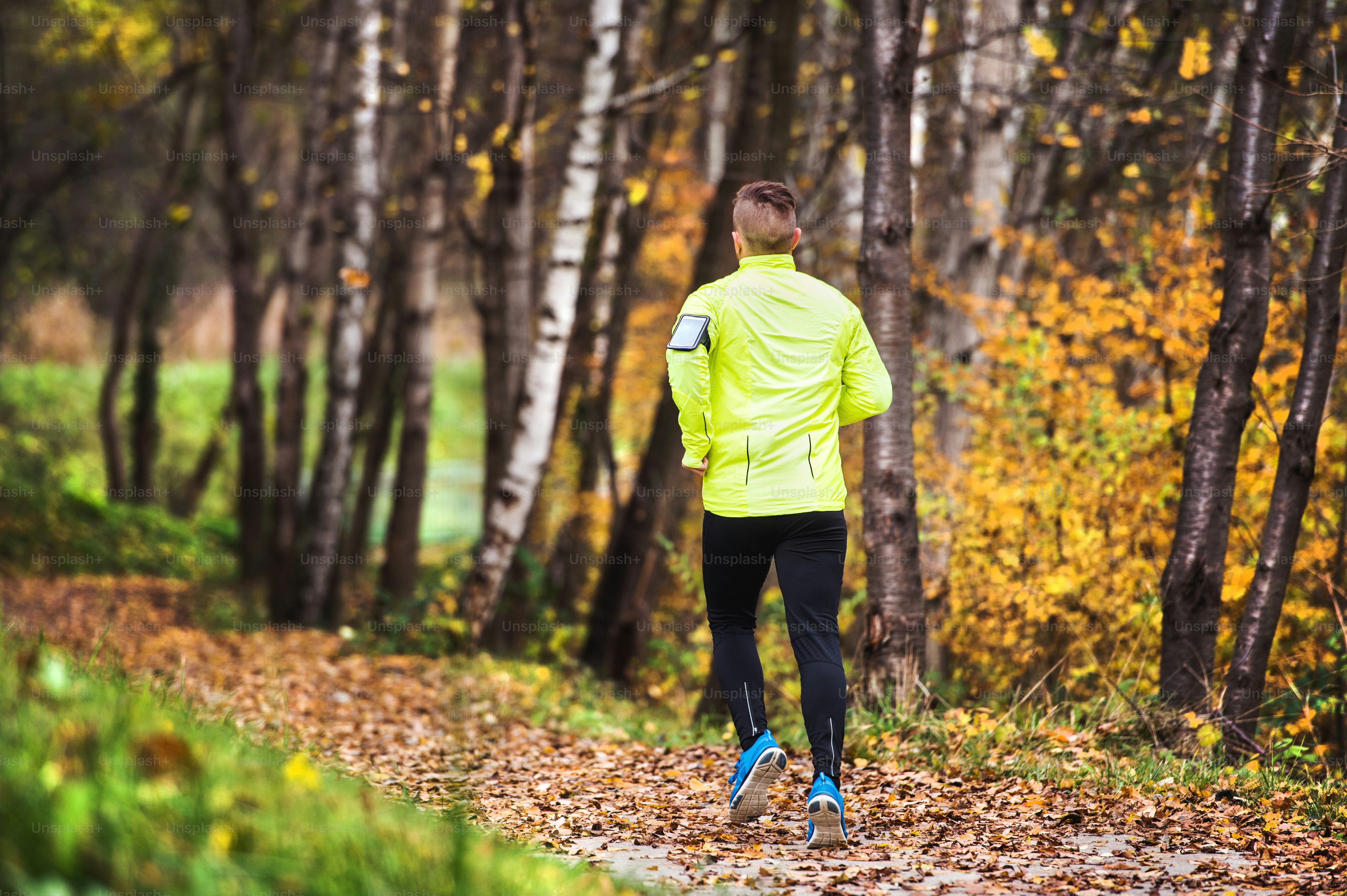 Young athlete with smartphone in yellow jacket running outside.Trail ...