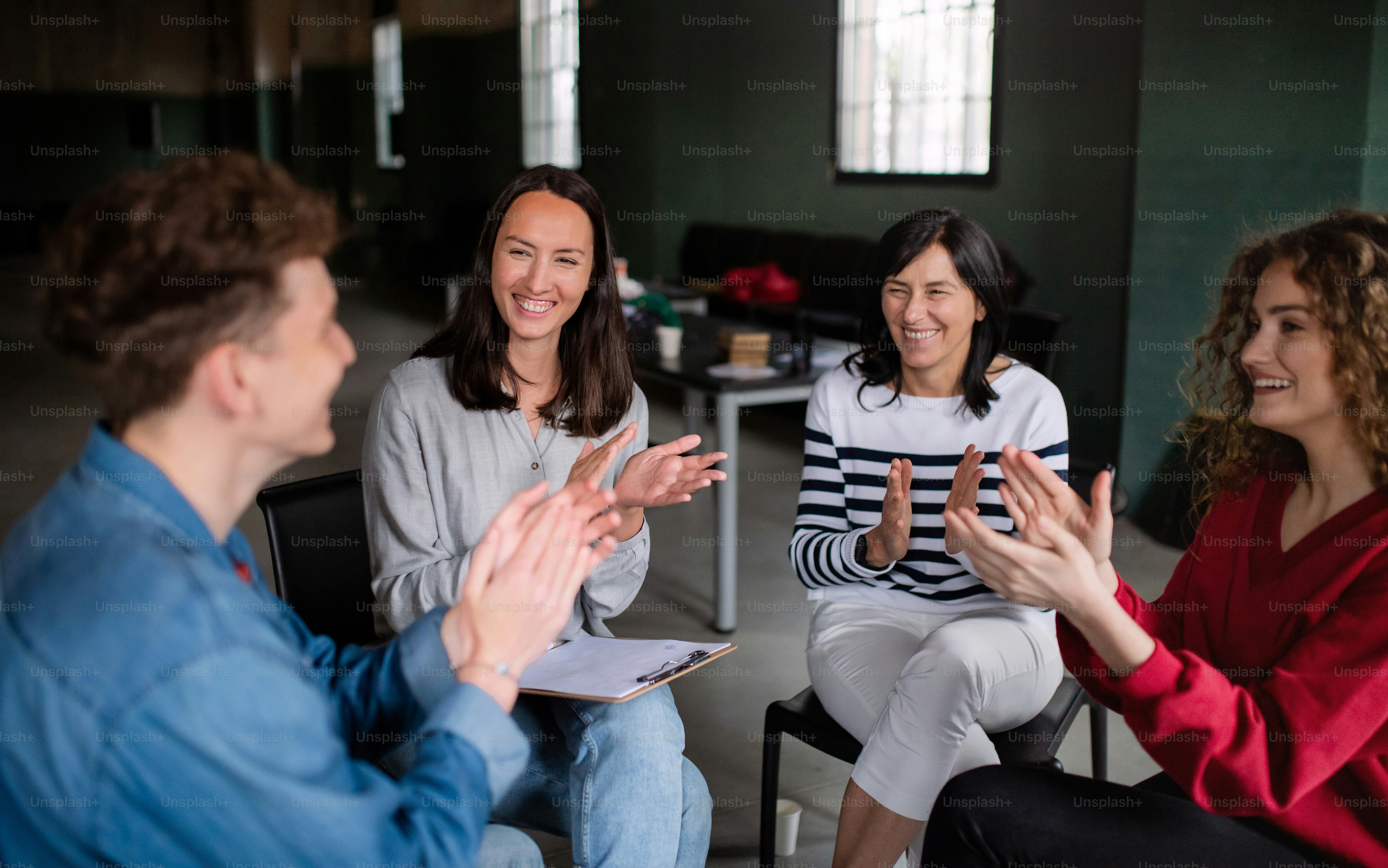 Happy men and women sitting in a circle during group therapy, reading and talking. photo ...