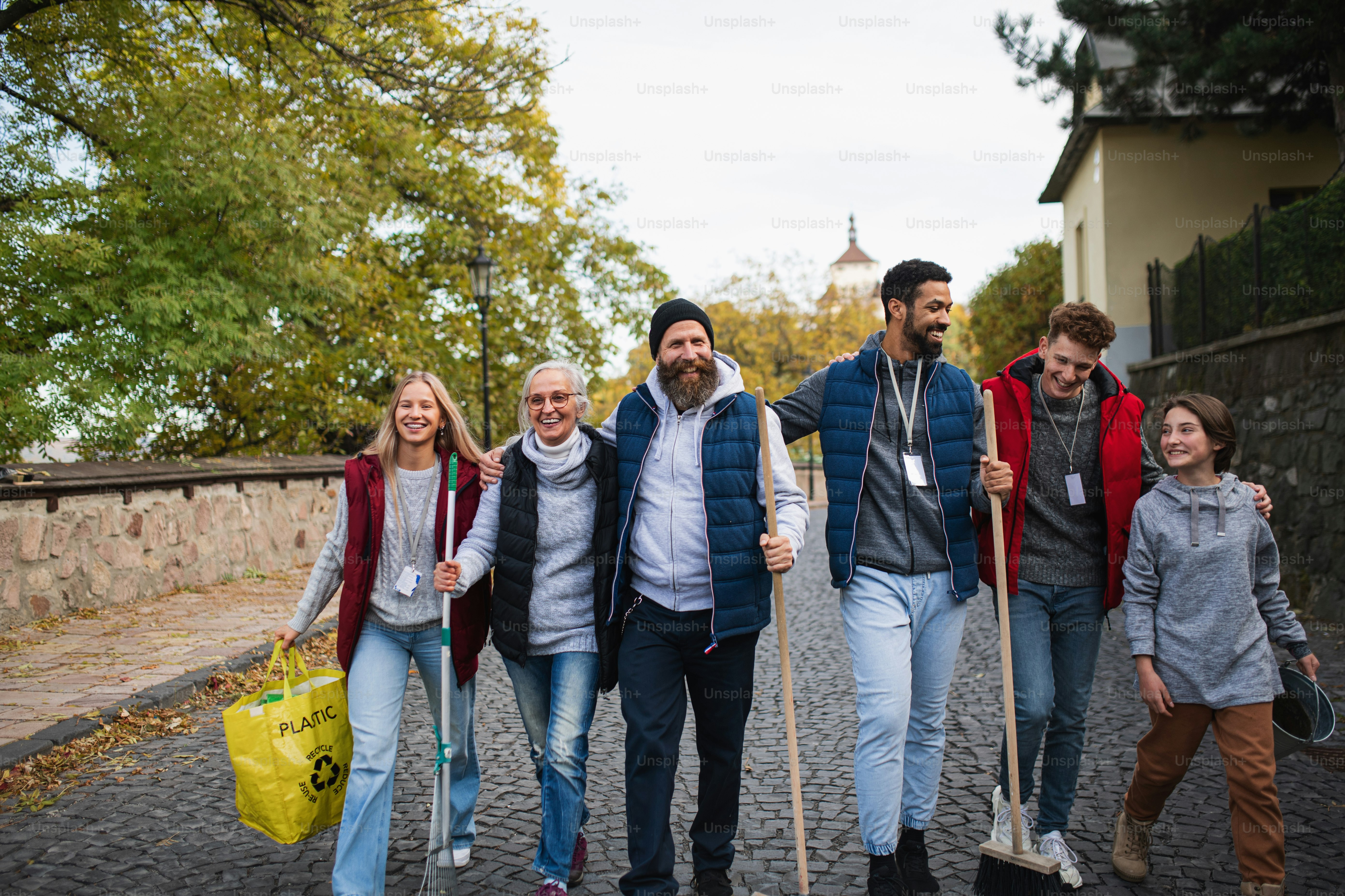 A diverse group of happy volunteers walking with tools to do street ...