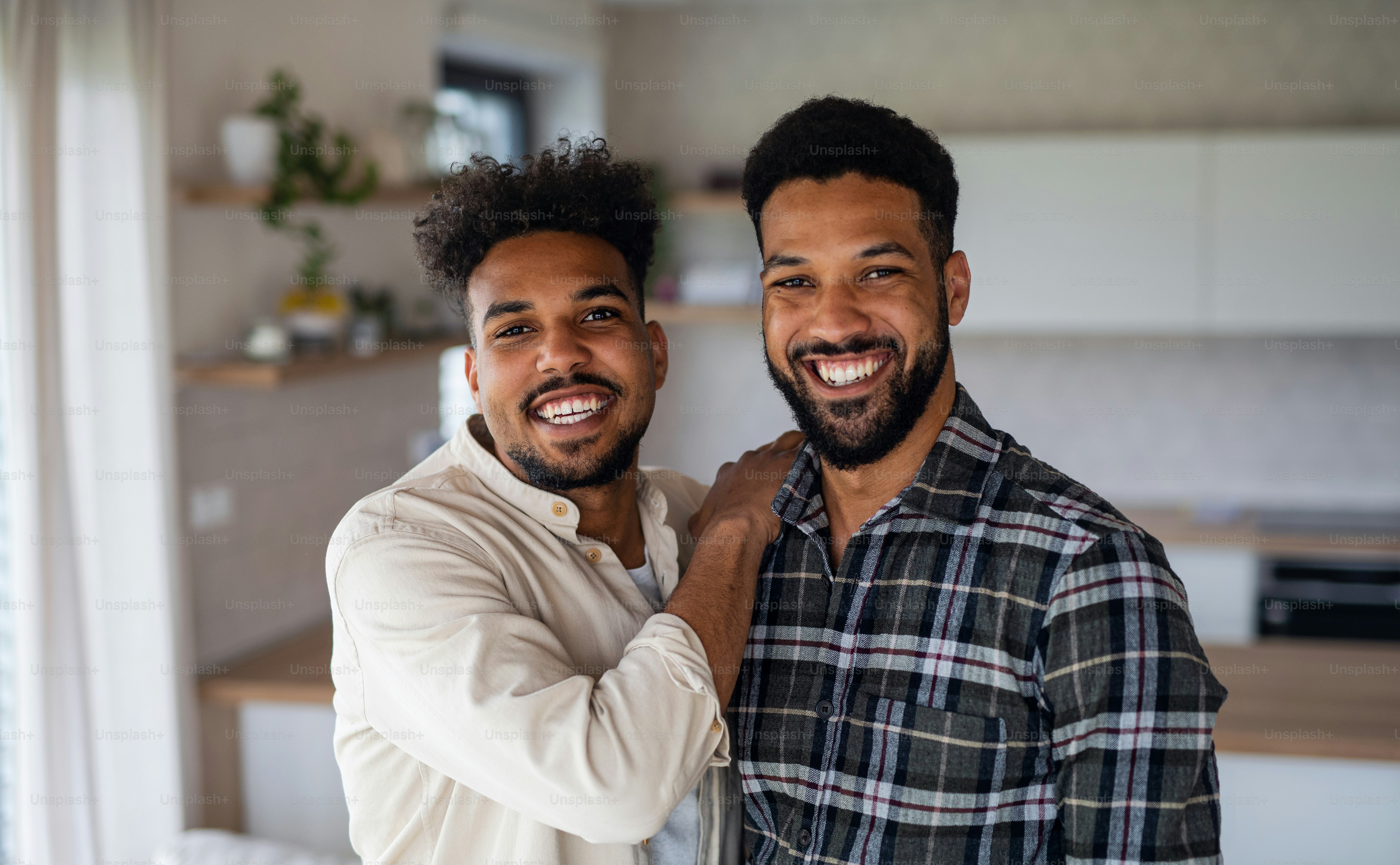 Portrait of young adult brothers in kitchen indoors at home, looking at ...