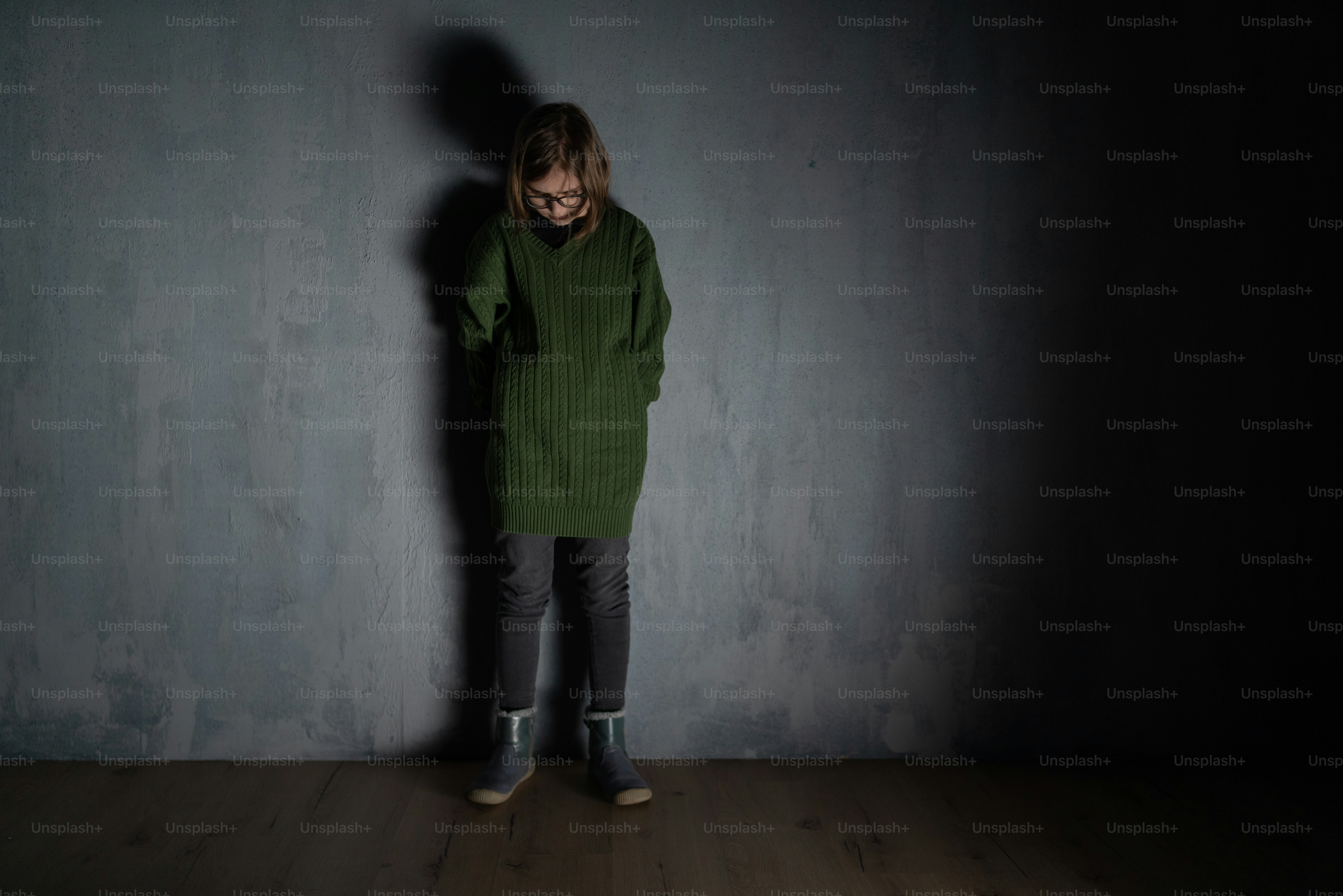 A sad little girl, alone in darkness, sitting and and covering face ...