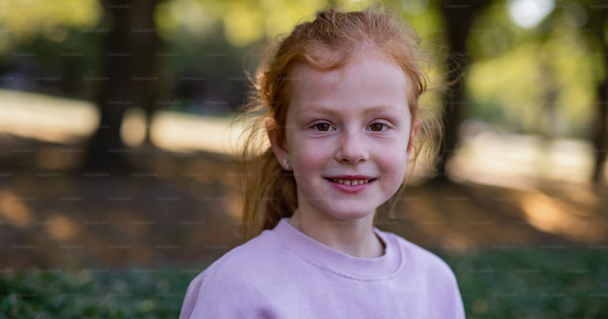 そばかすと赤い髪の幸せな女の子がカメラを見て、公園の外で微笑んでいます。の写真 Unsplashのそばかすの画像