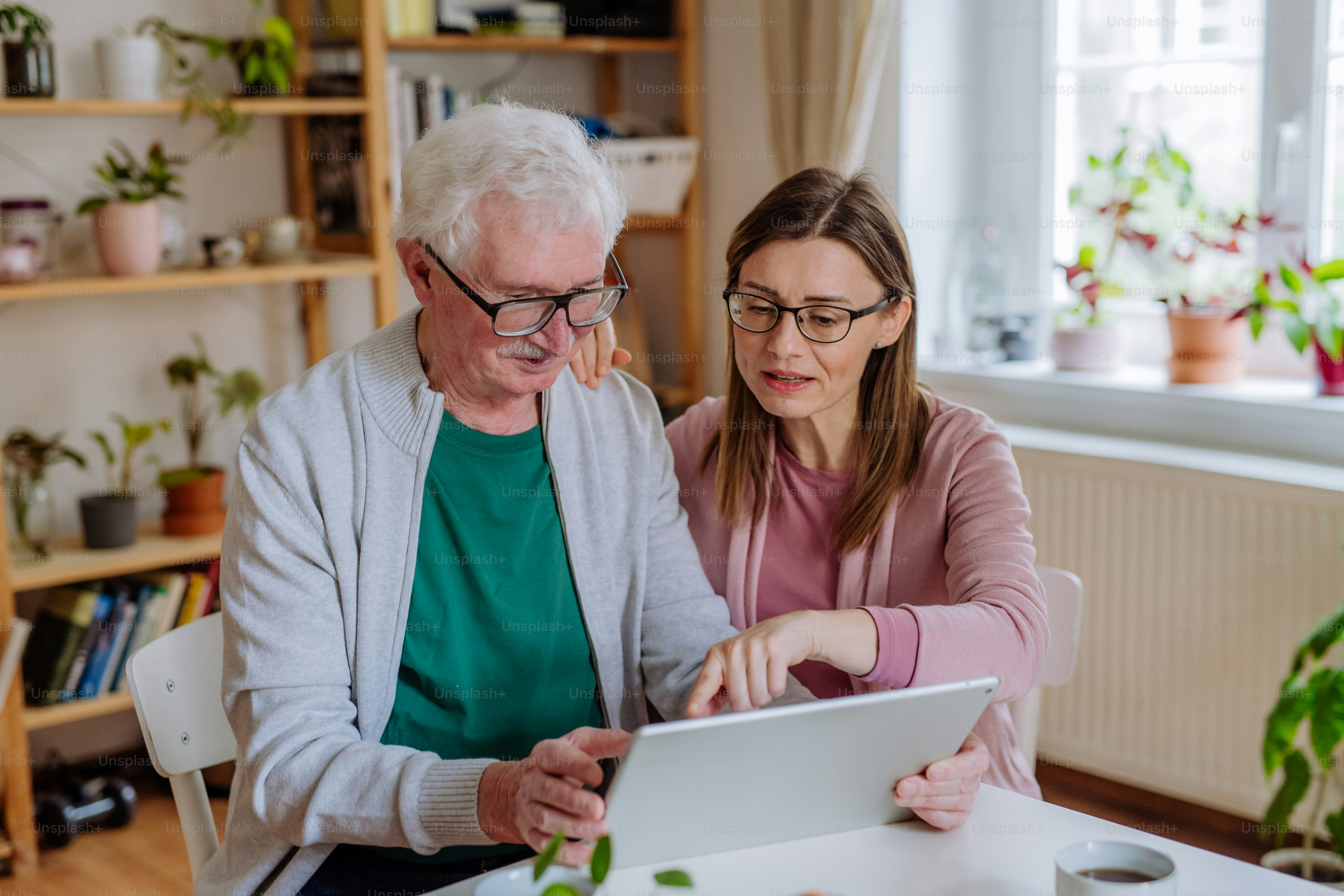 An adult daughter visiting her senior father at home and using tablet ...