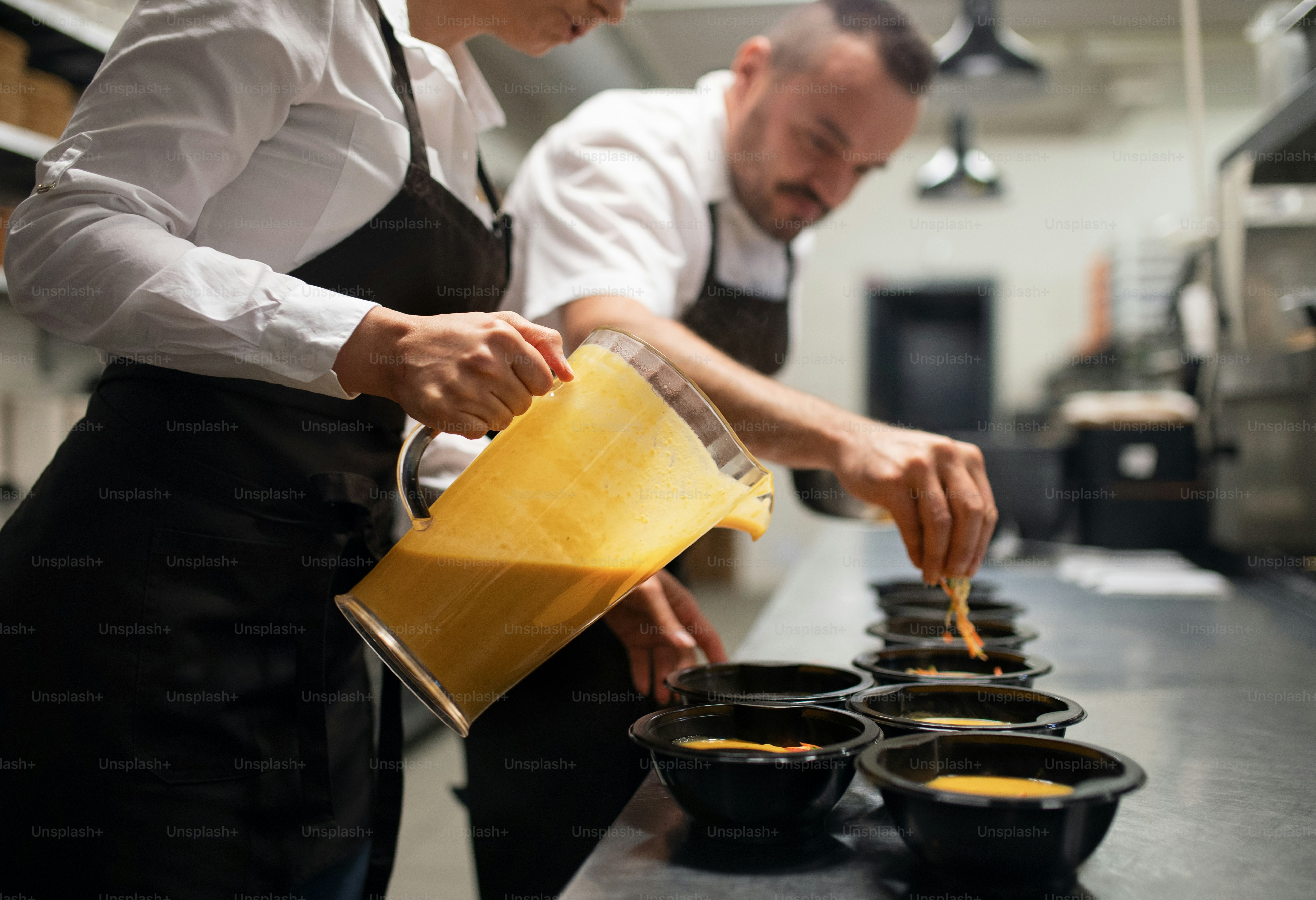 A chef and cook serving soup together indoors in restaurant kitchen ...