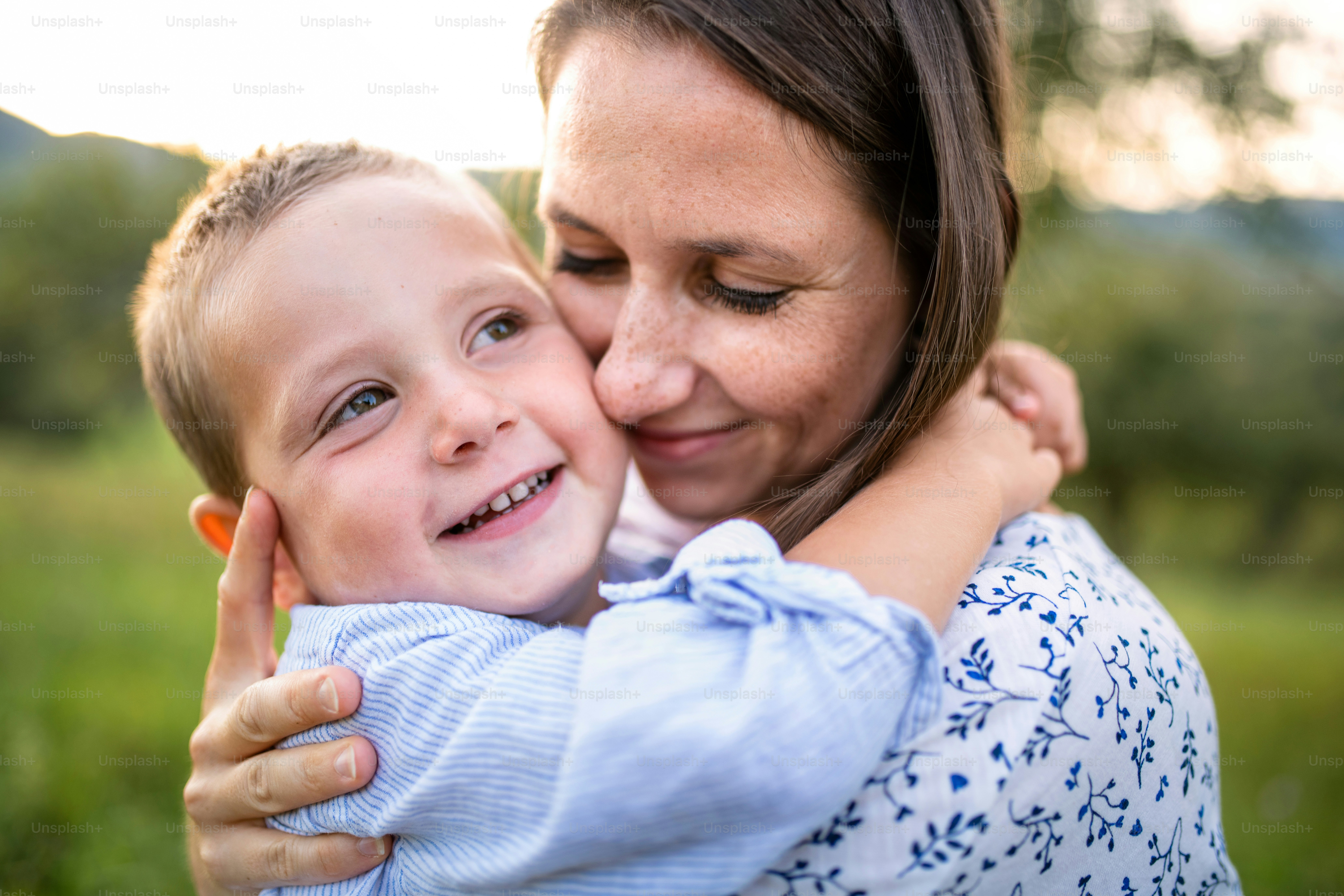A mother with small toddler son on walk on meadow outdoors, hugging ...