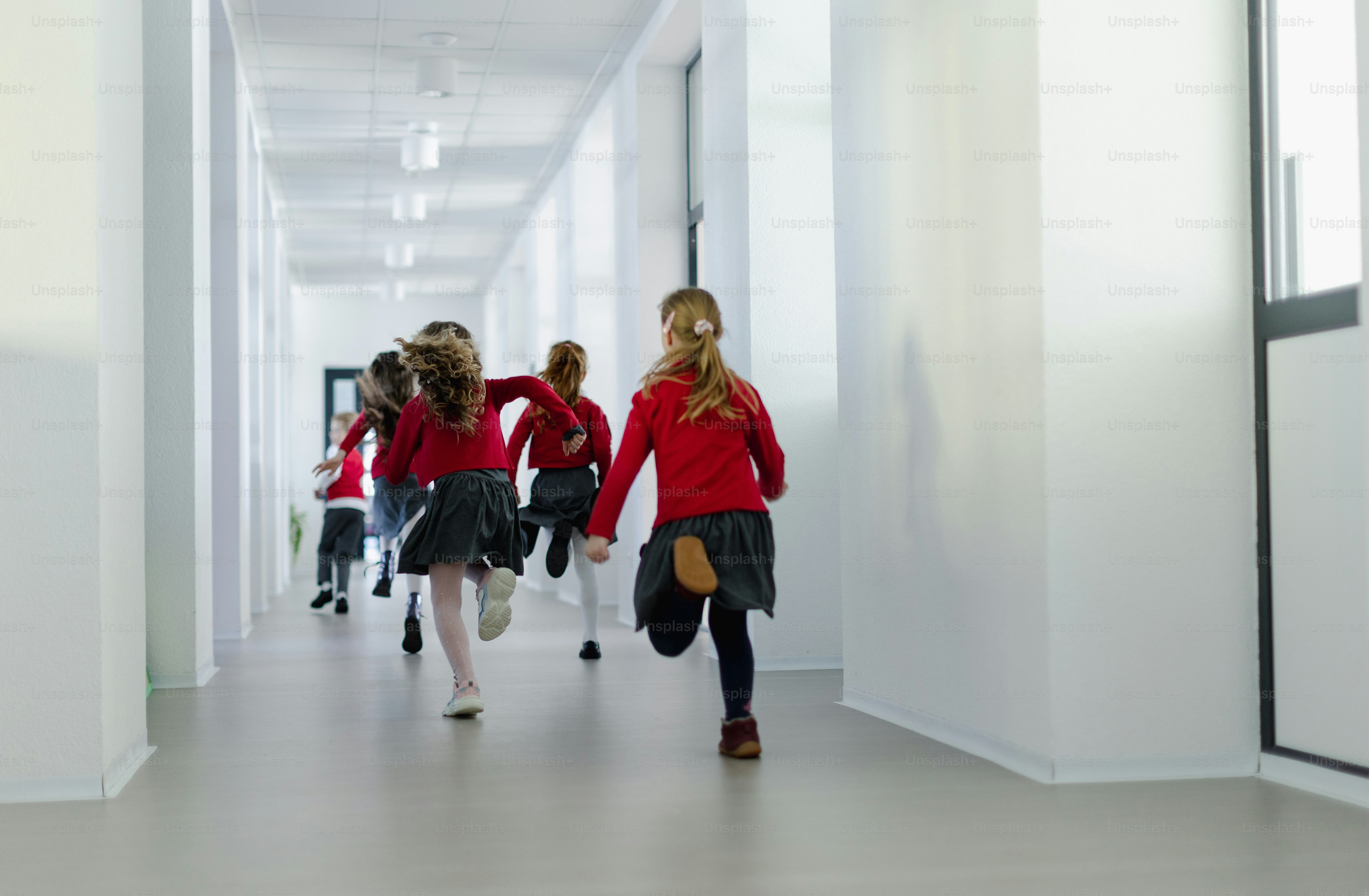 A rear view of schoolchildren in uniforms running in school corridor ...