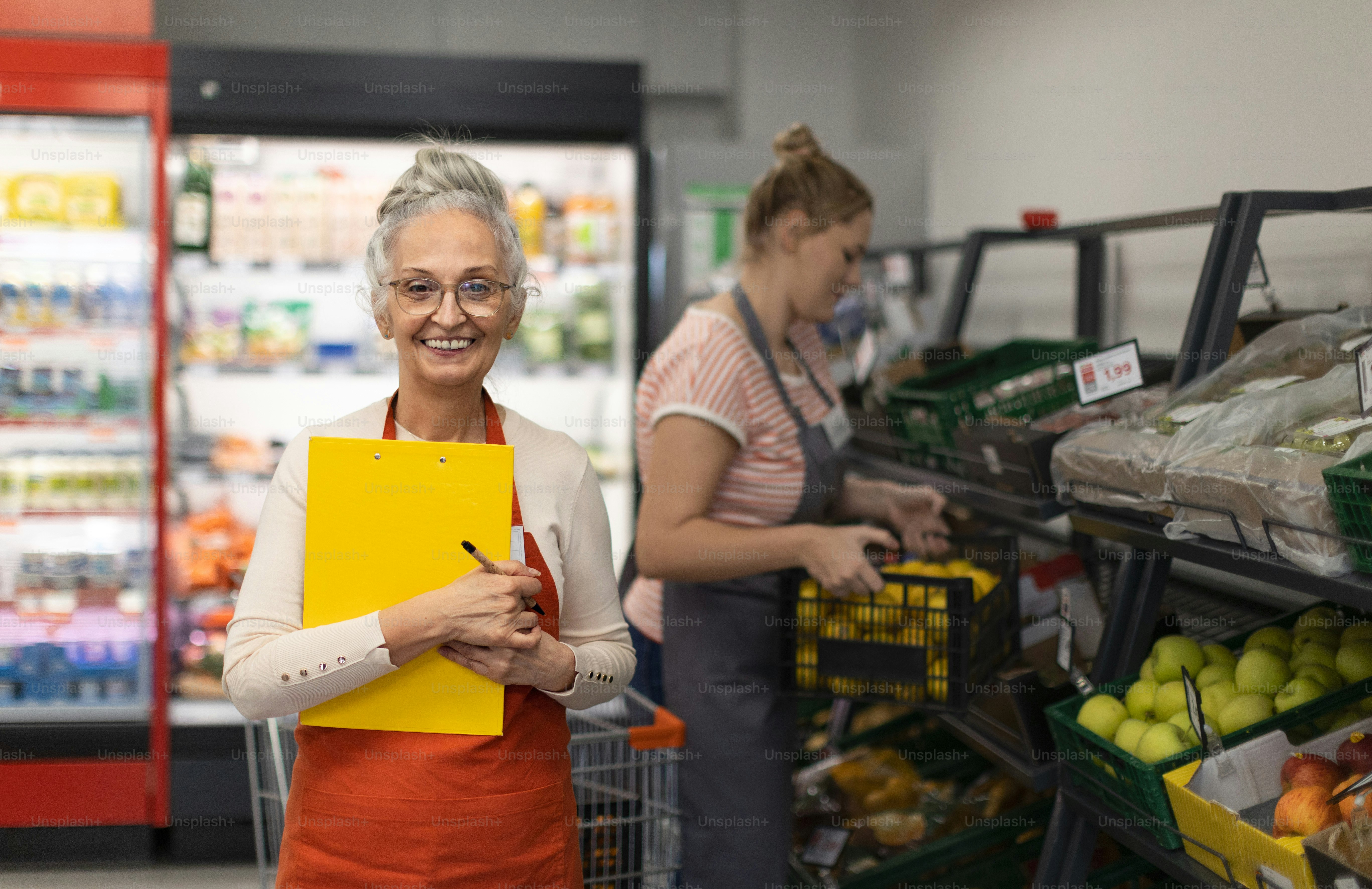 A confident senior shop assistant in supermarket in vegetable shell, in ...