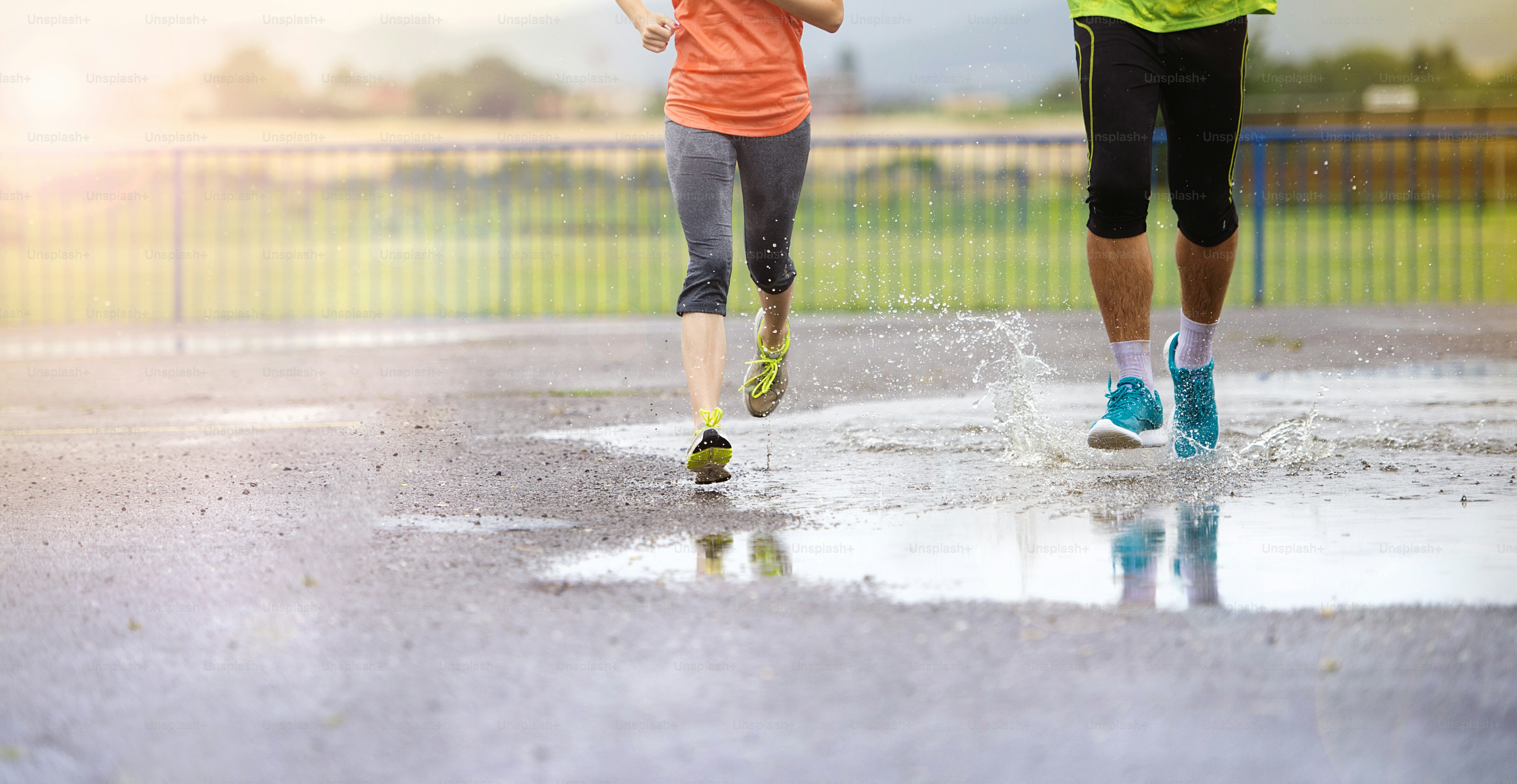 Young couple running on asphalt sports field in rainy weather. Details ...