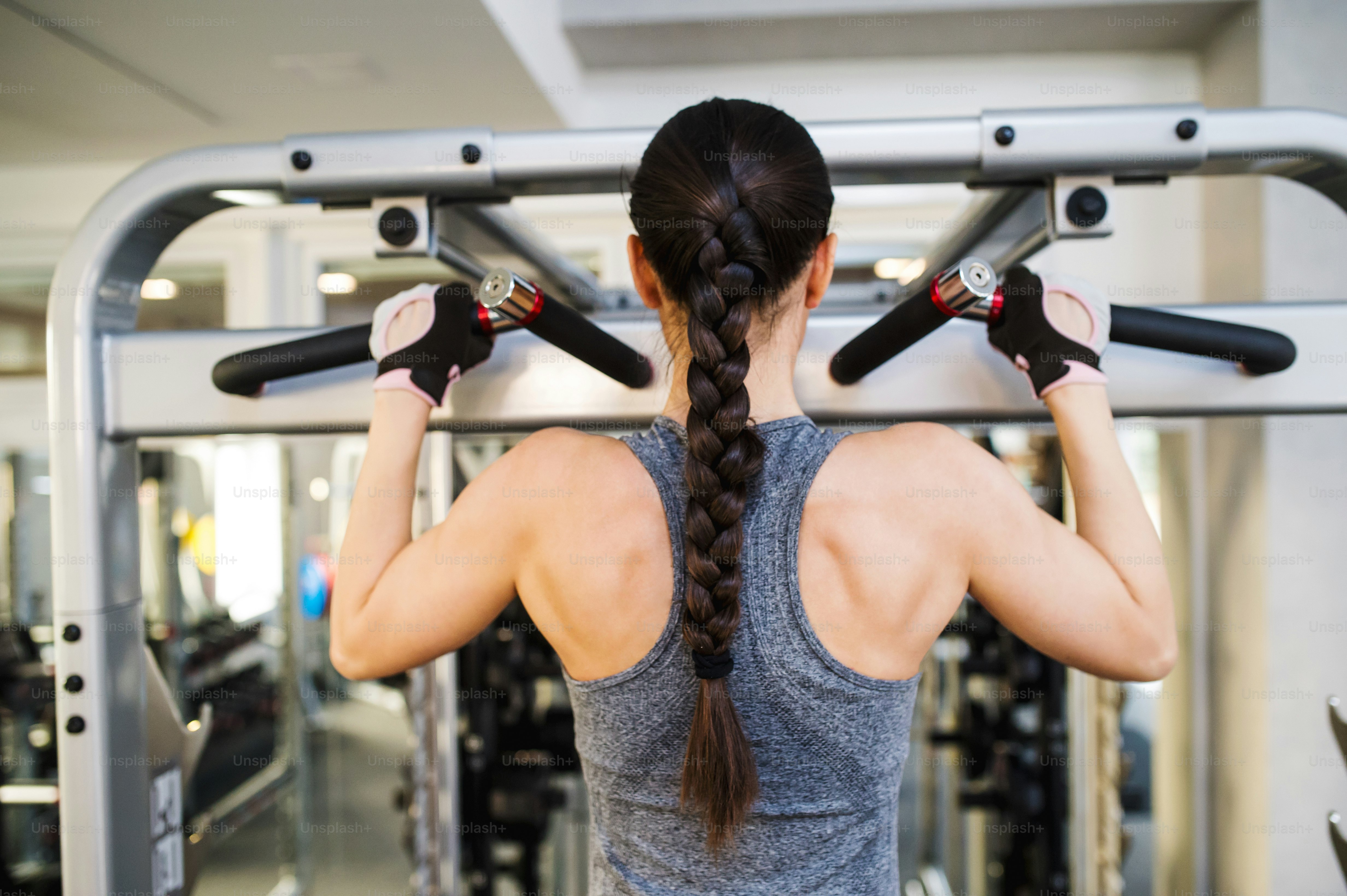 Close up of attractive fit woman flexing back muscles on cable machine ...