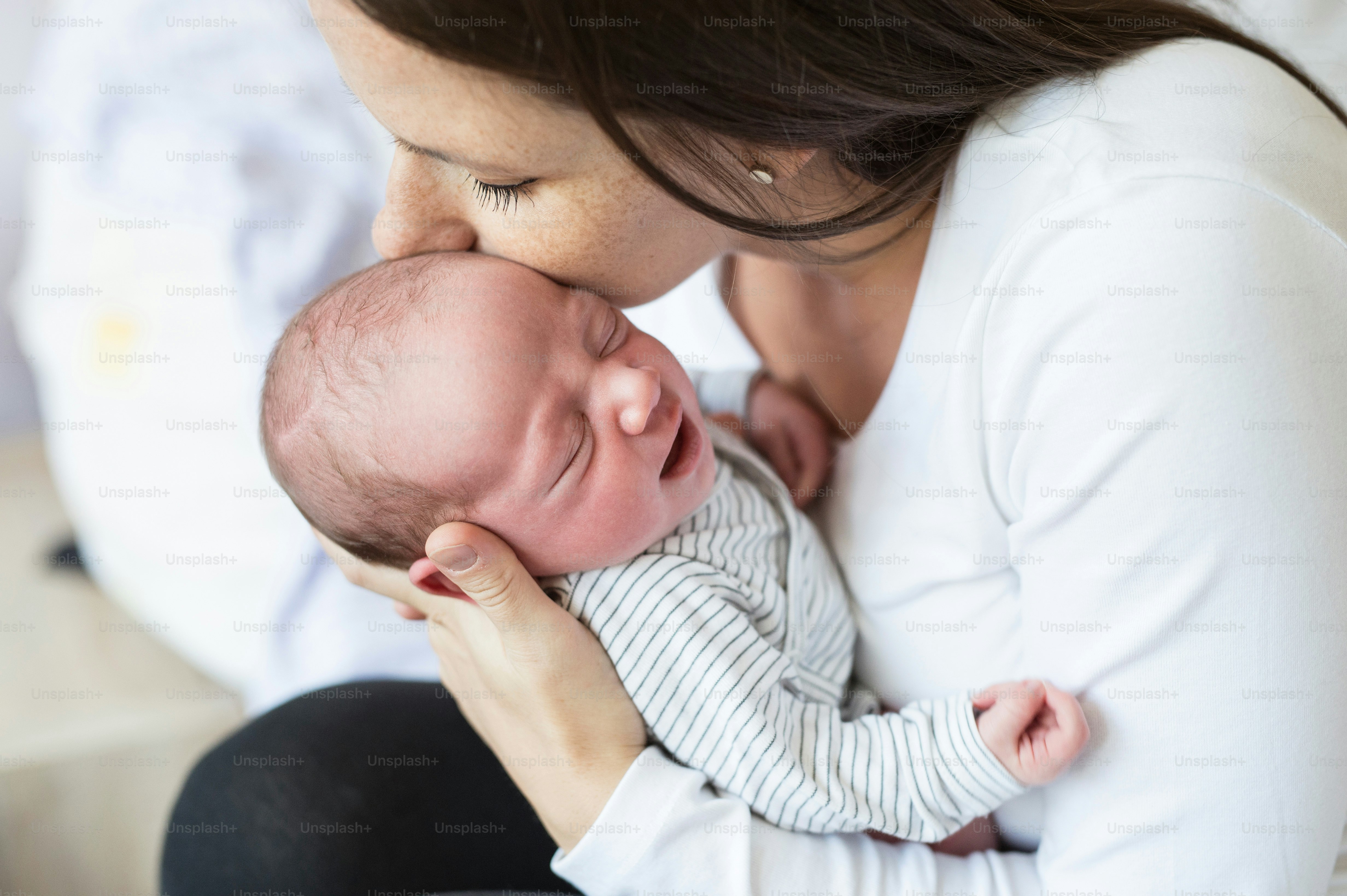 Beautiful young mother with her newborn baby son, sitting on bed in ...