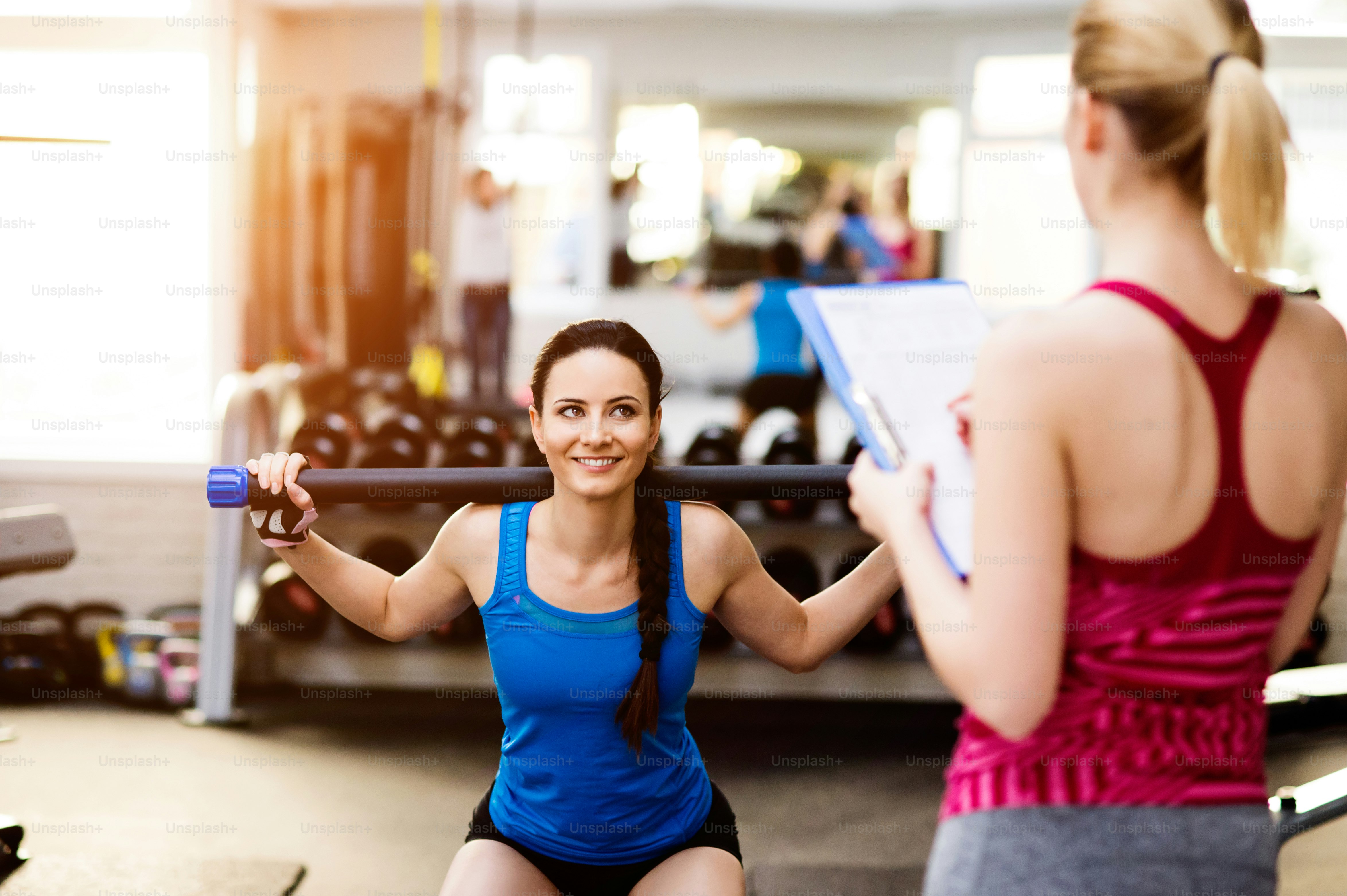 Close up of an attractive fit woman in blue singlet exercising in a gym with her personal ...