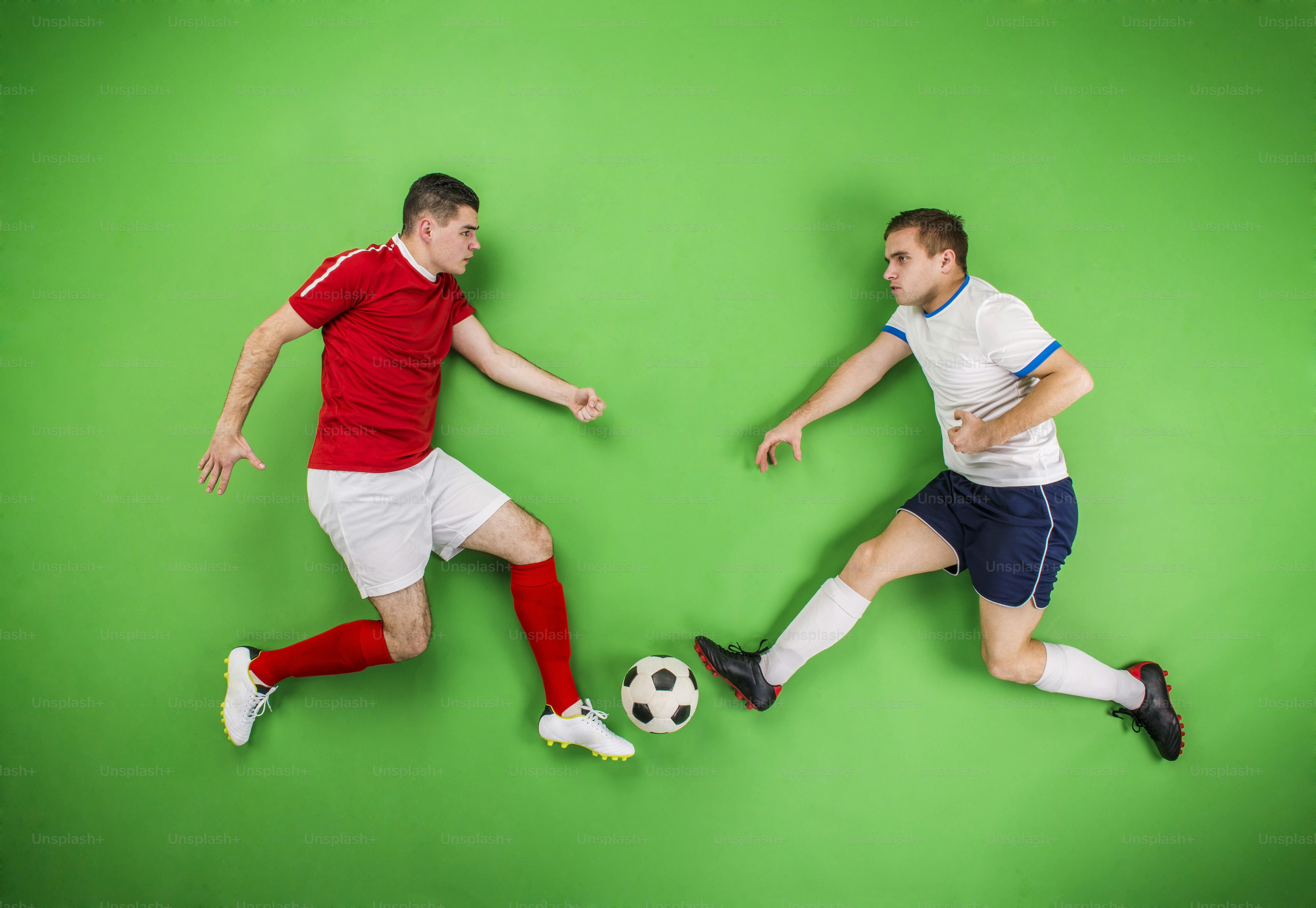 Two football players fighting for a ball. Studio shot on a green ...