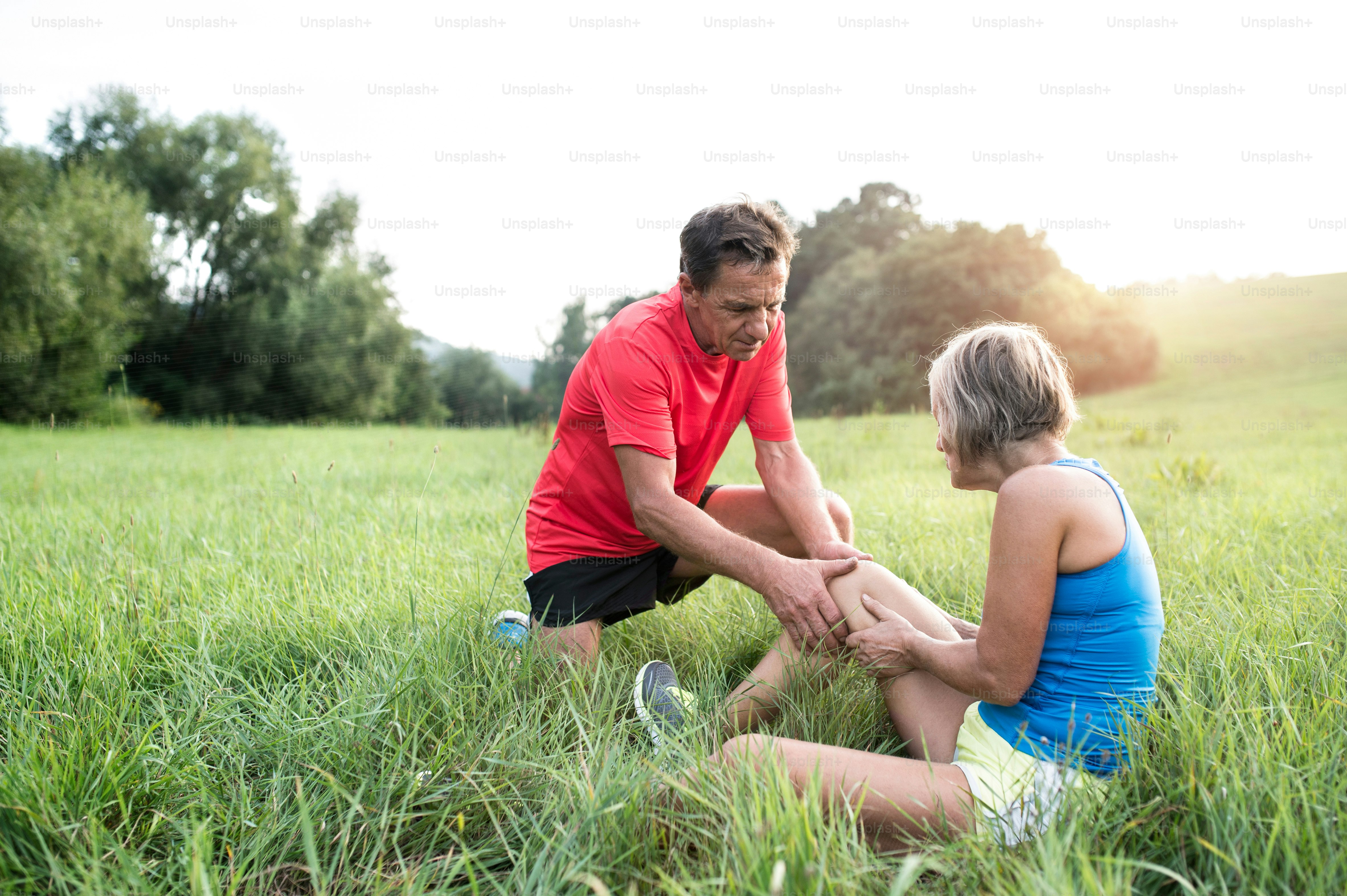 Active senior runners outside in field. Woman with injured knee. Man ...