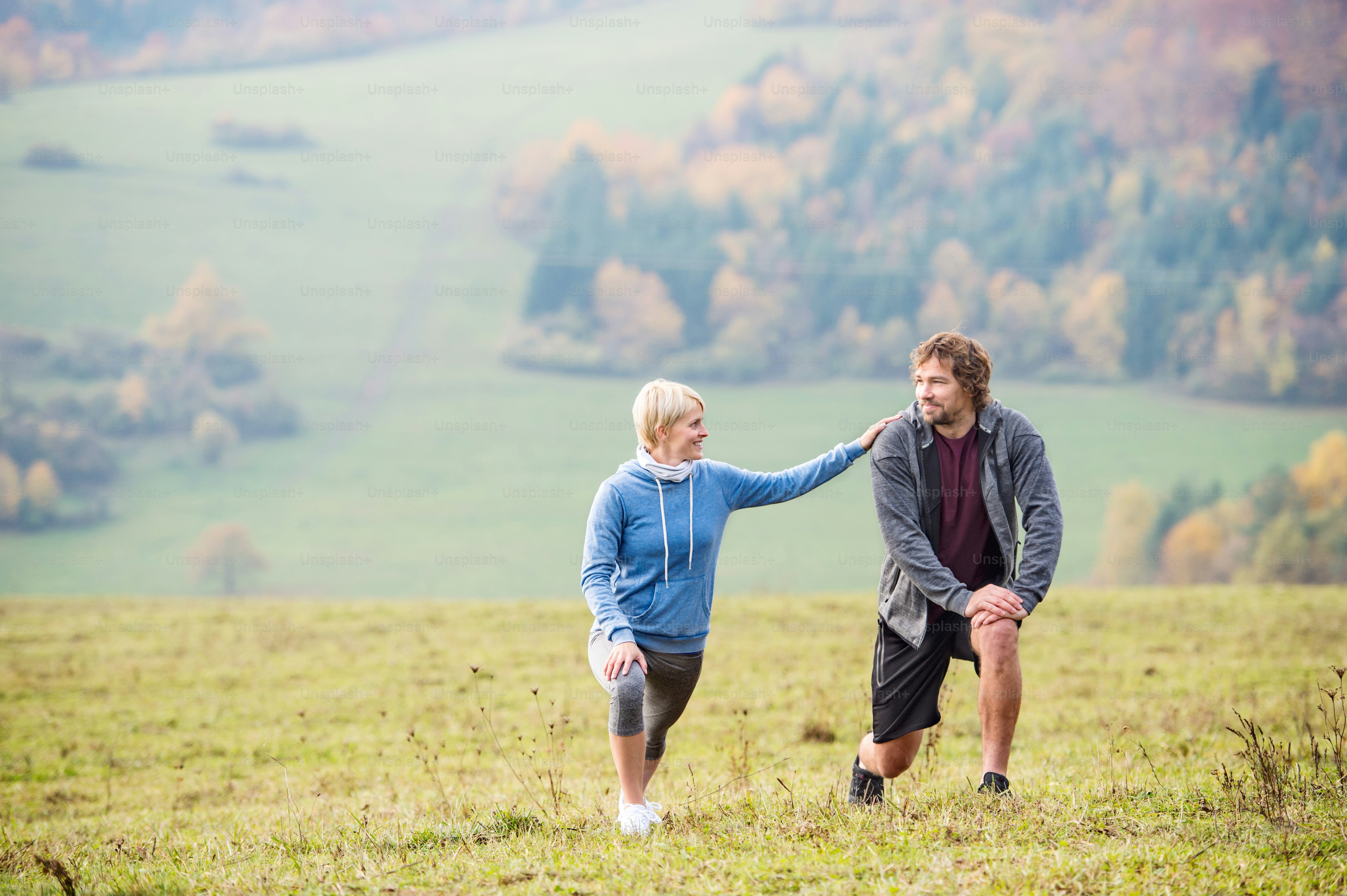Two young beautiful runners in colorful autumn nature, stretching legs ...