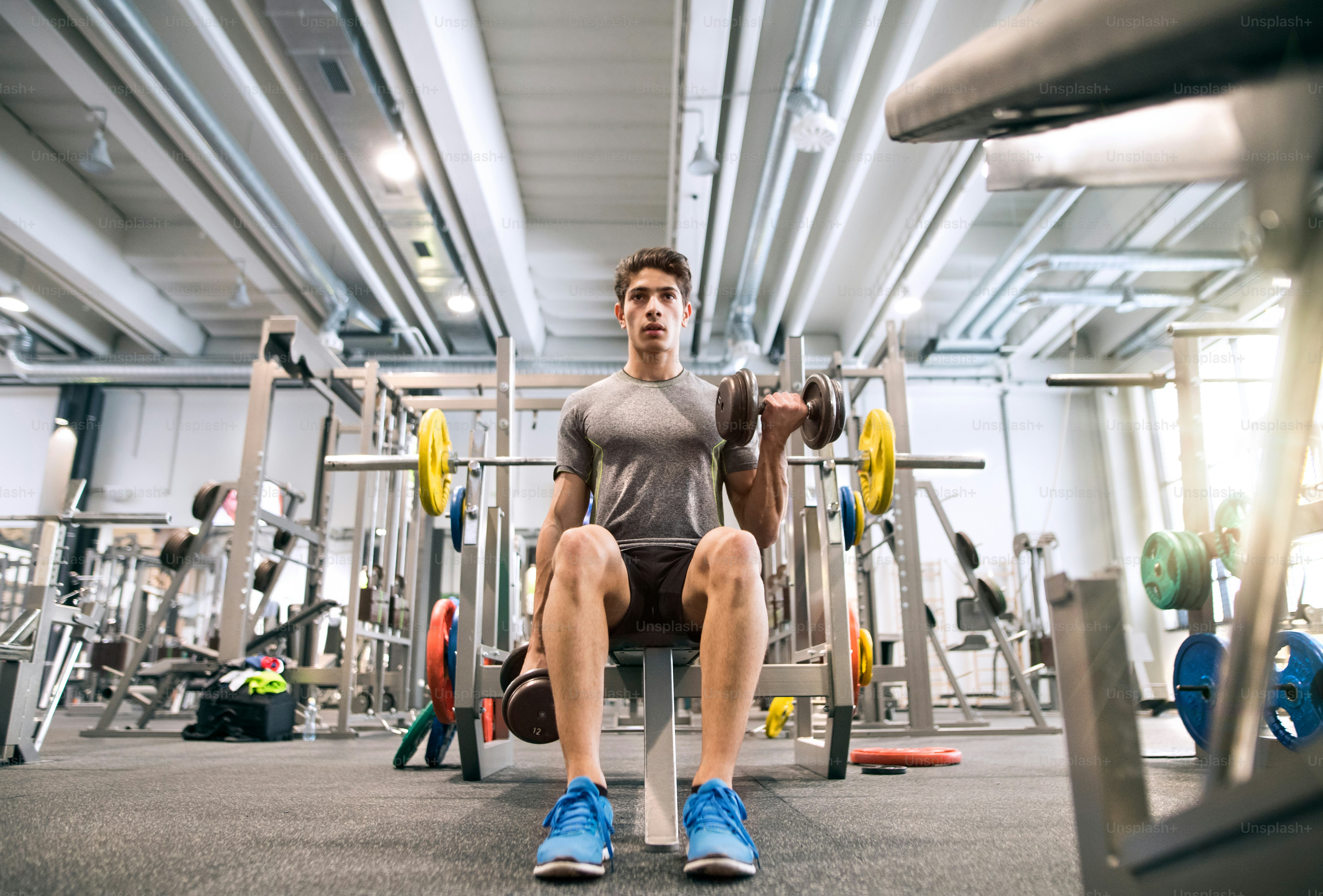 Young hispanic fitness man in gym sitting on bench, working out with ...
