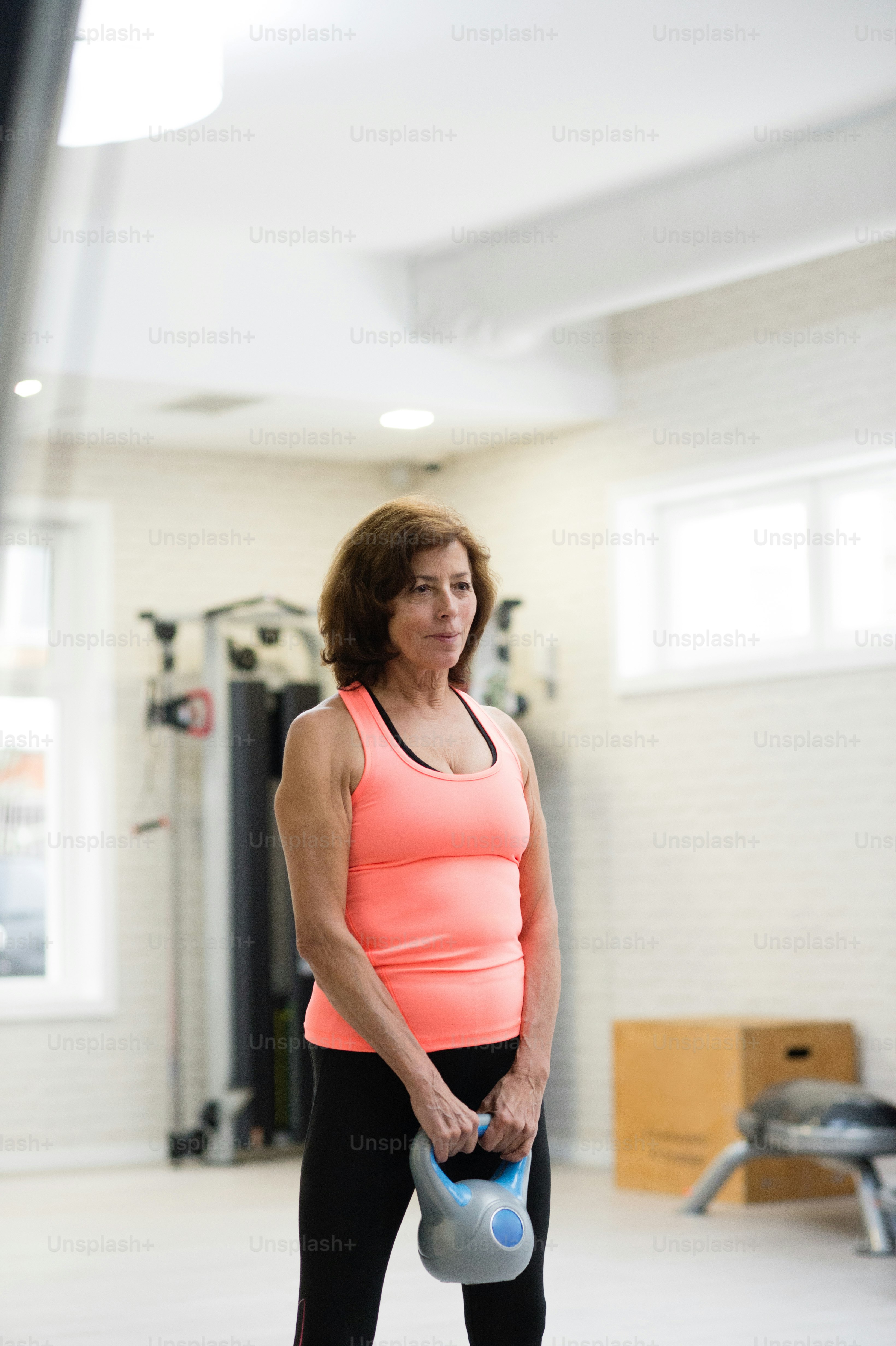 Beautiful fit senior woman in gym working out using kettlebells. Sport ...