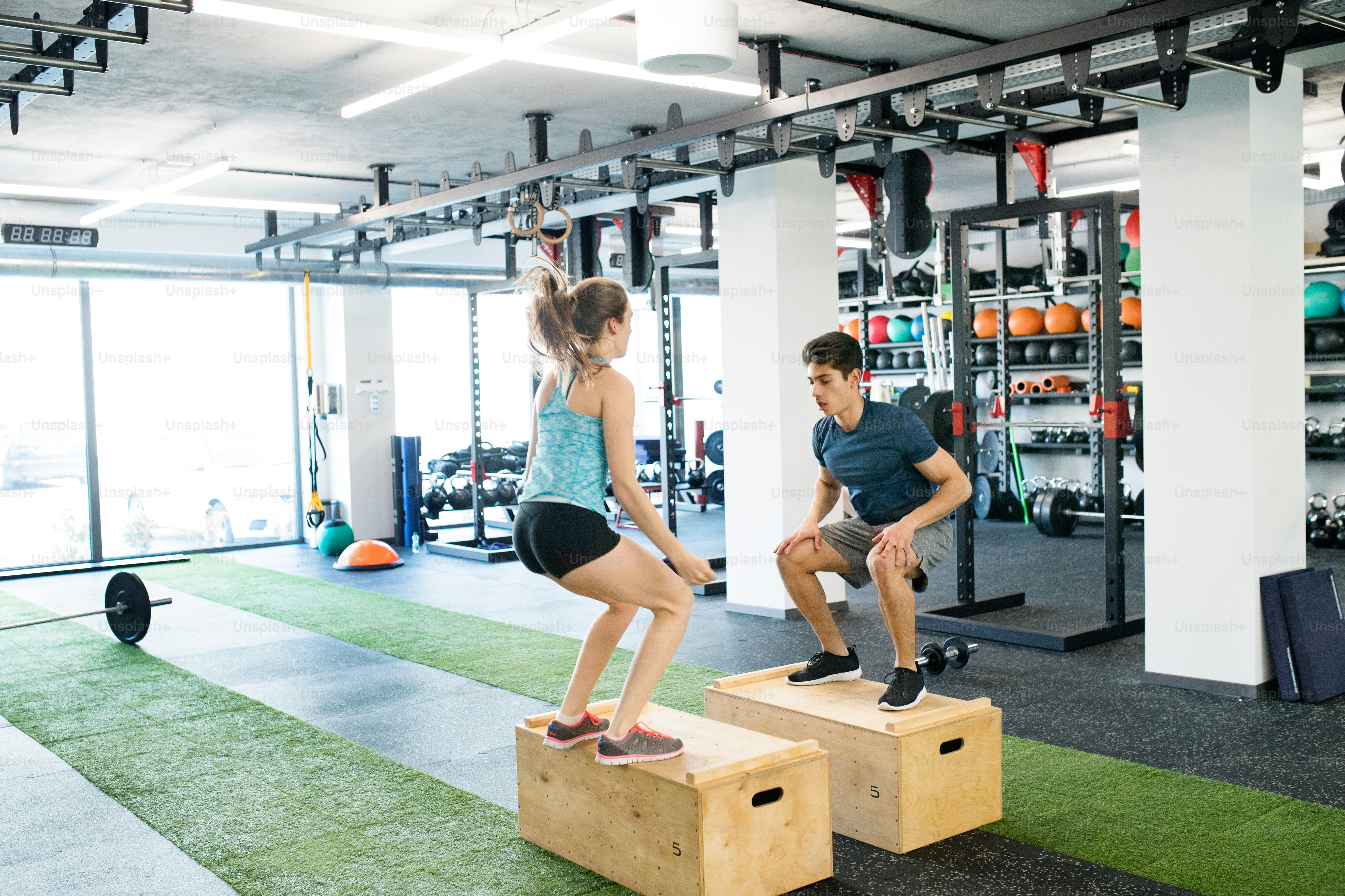 Beautiful young fit couple exercising in modern gym, doing box jumps ...