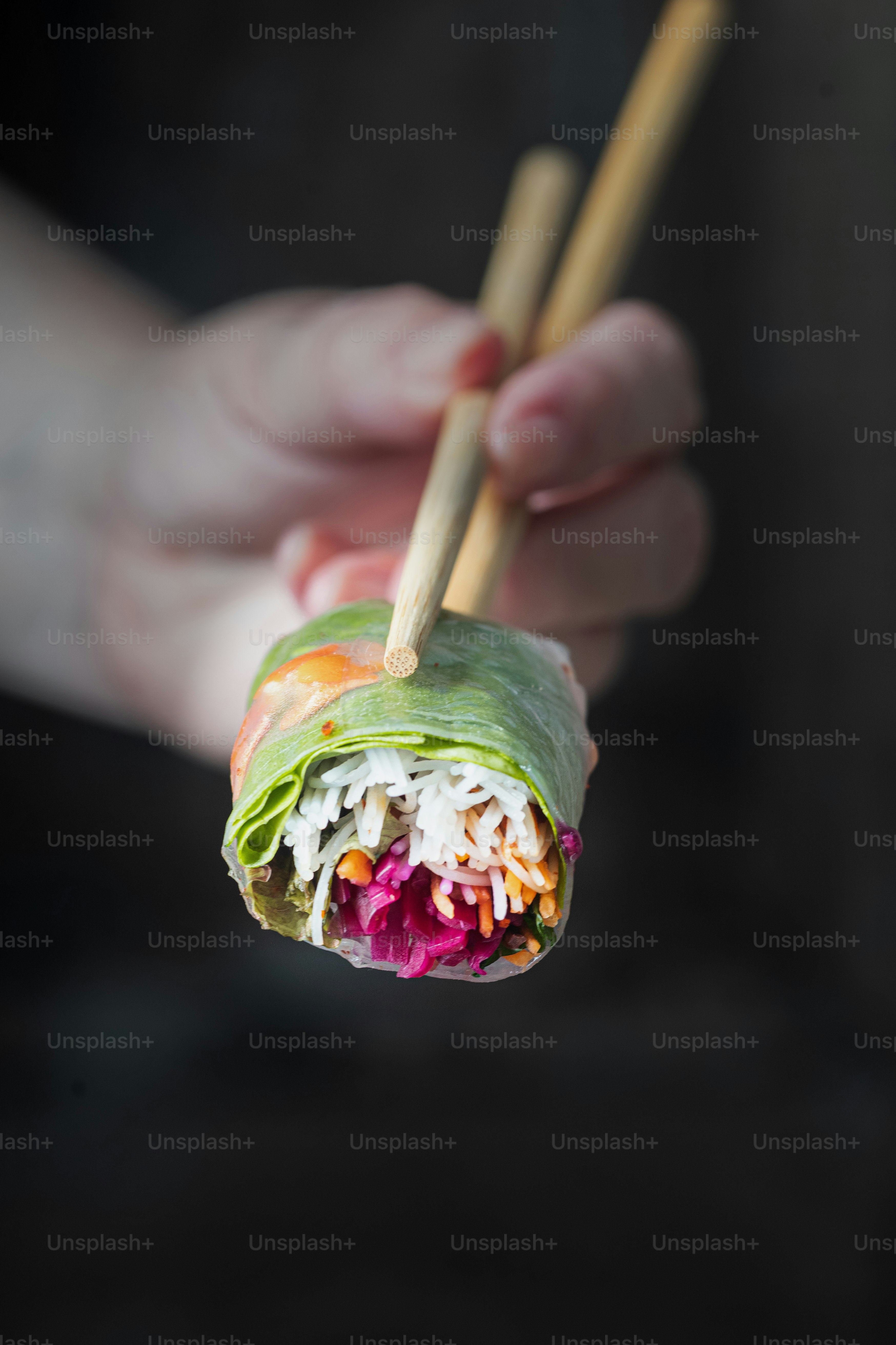 A person holding a sushi roll with chopsticks photo – Spring rolls ...