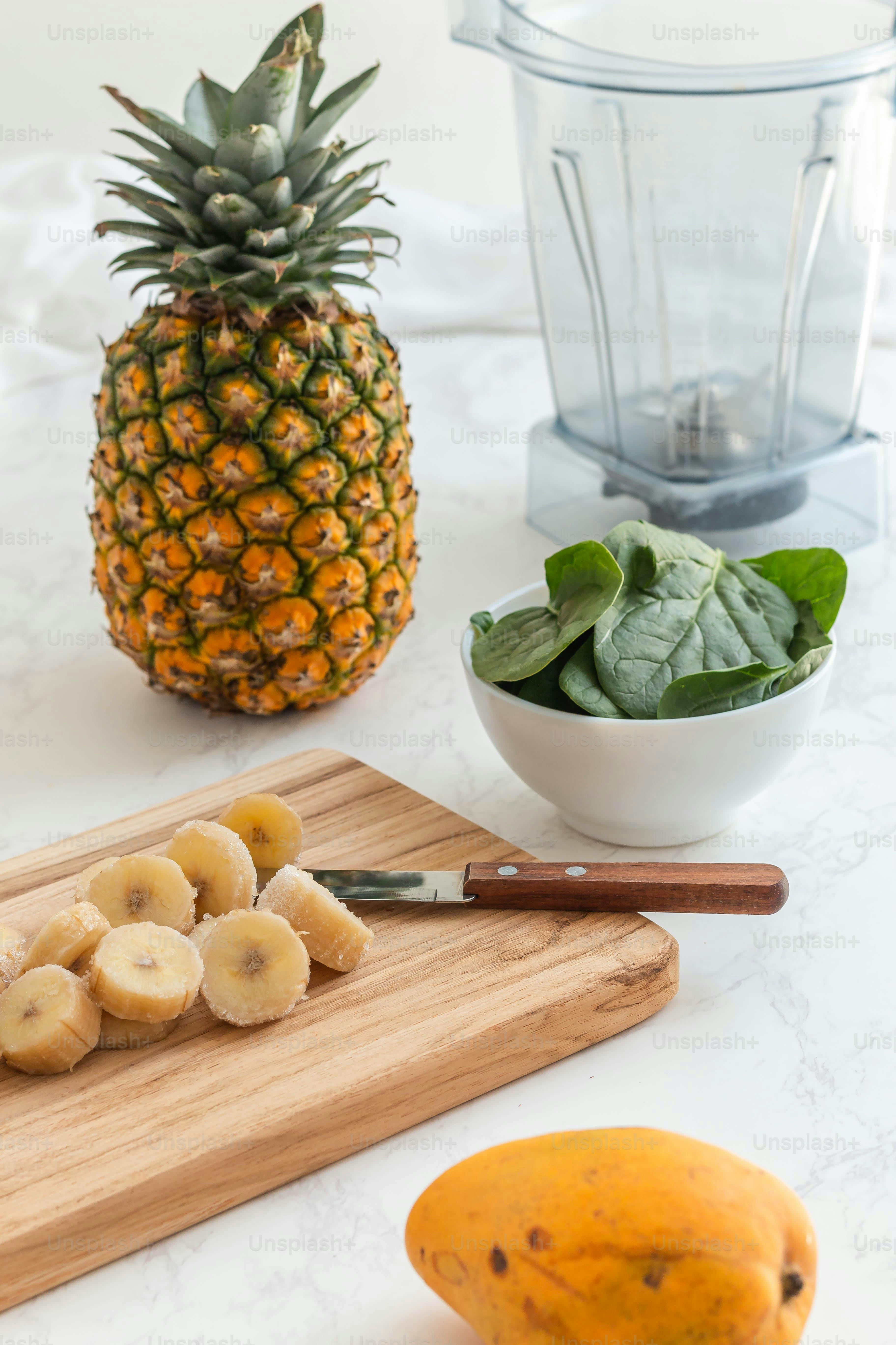 A pineapple and bananas on a cutting board next to a blender photo ...
