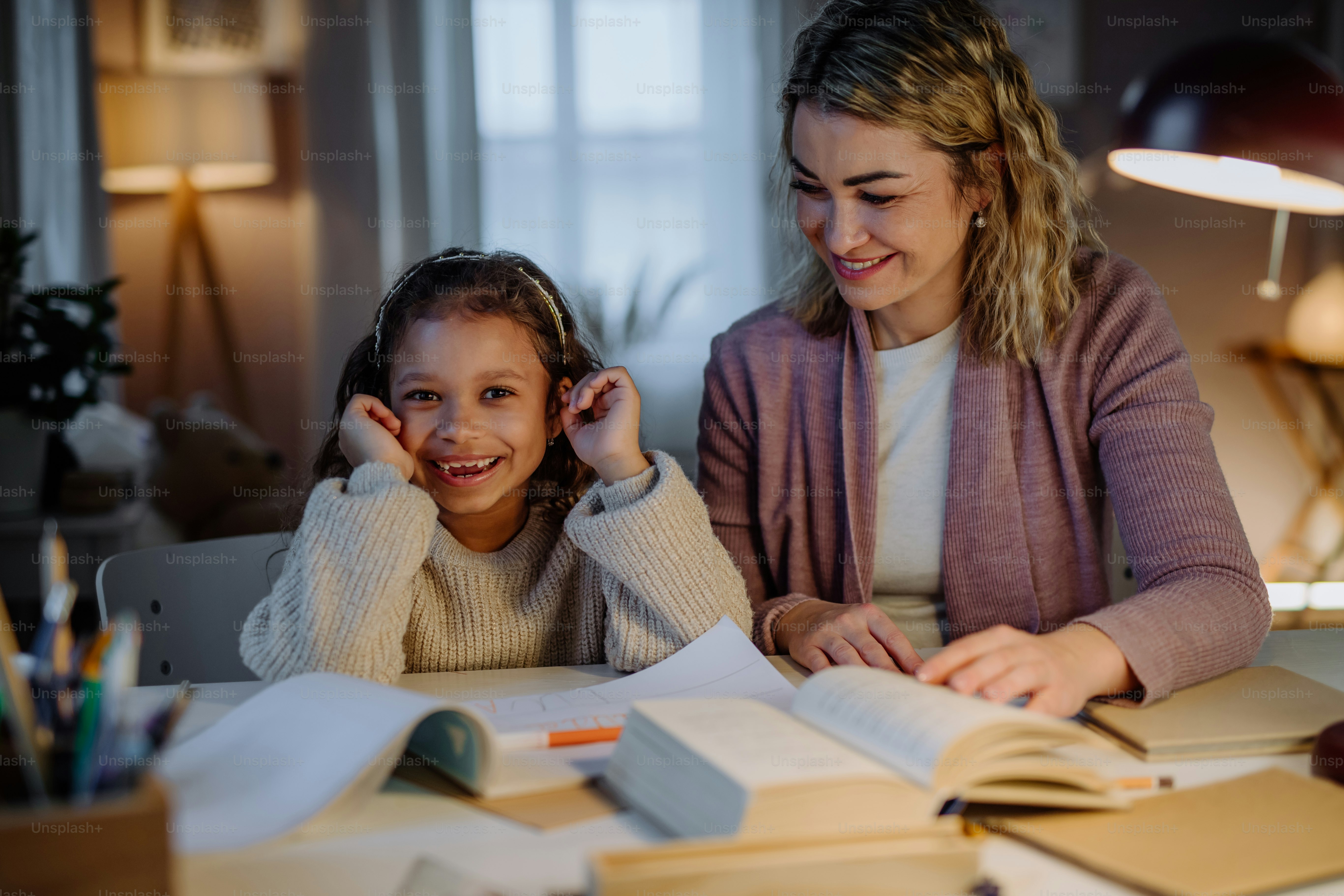 A happy little girl doing homework with her mother and looking at ...